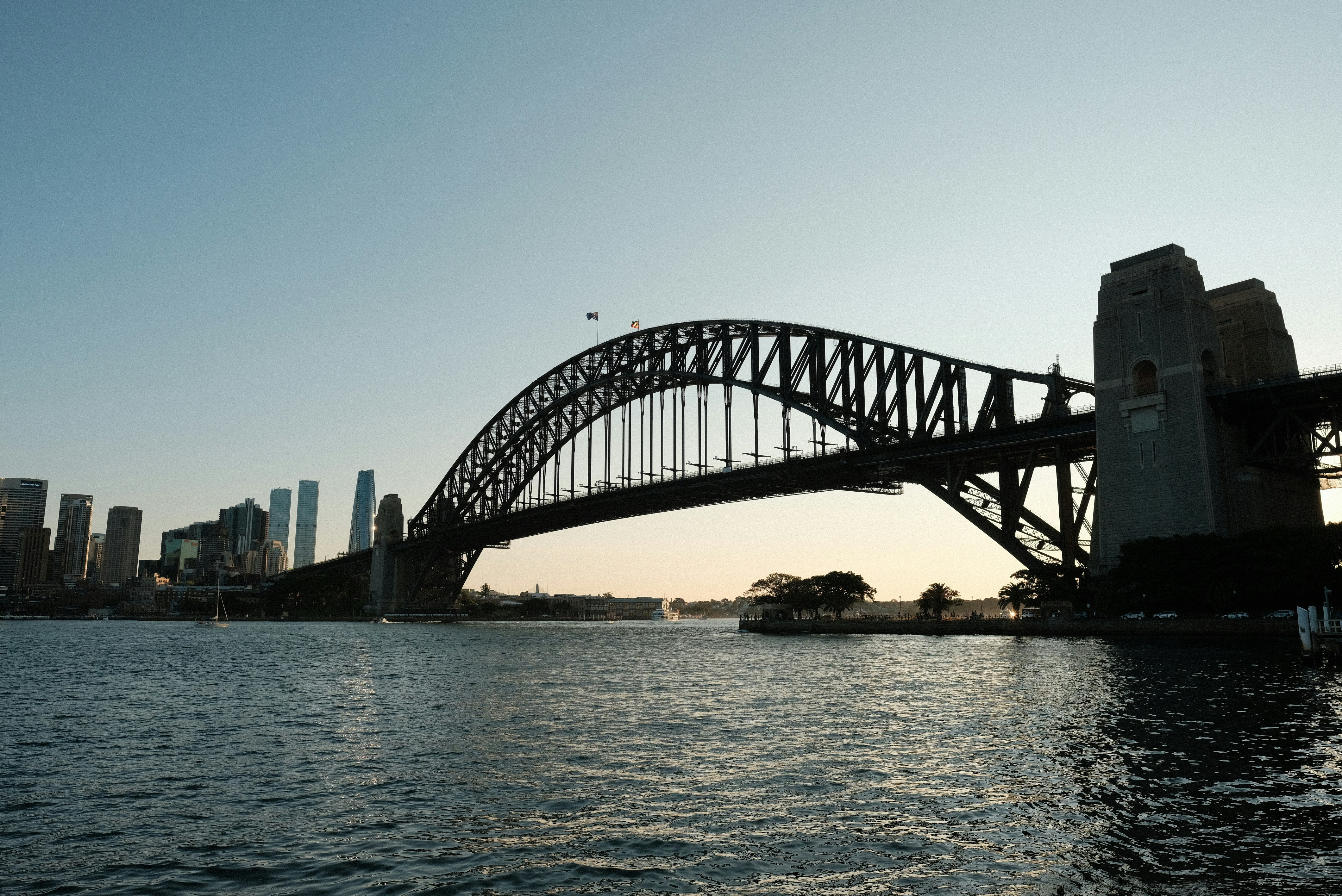 Sydney Harbour Bridge silhouetted against a serene sunset with a city skyline backdrop.
