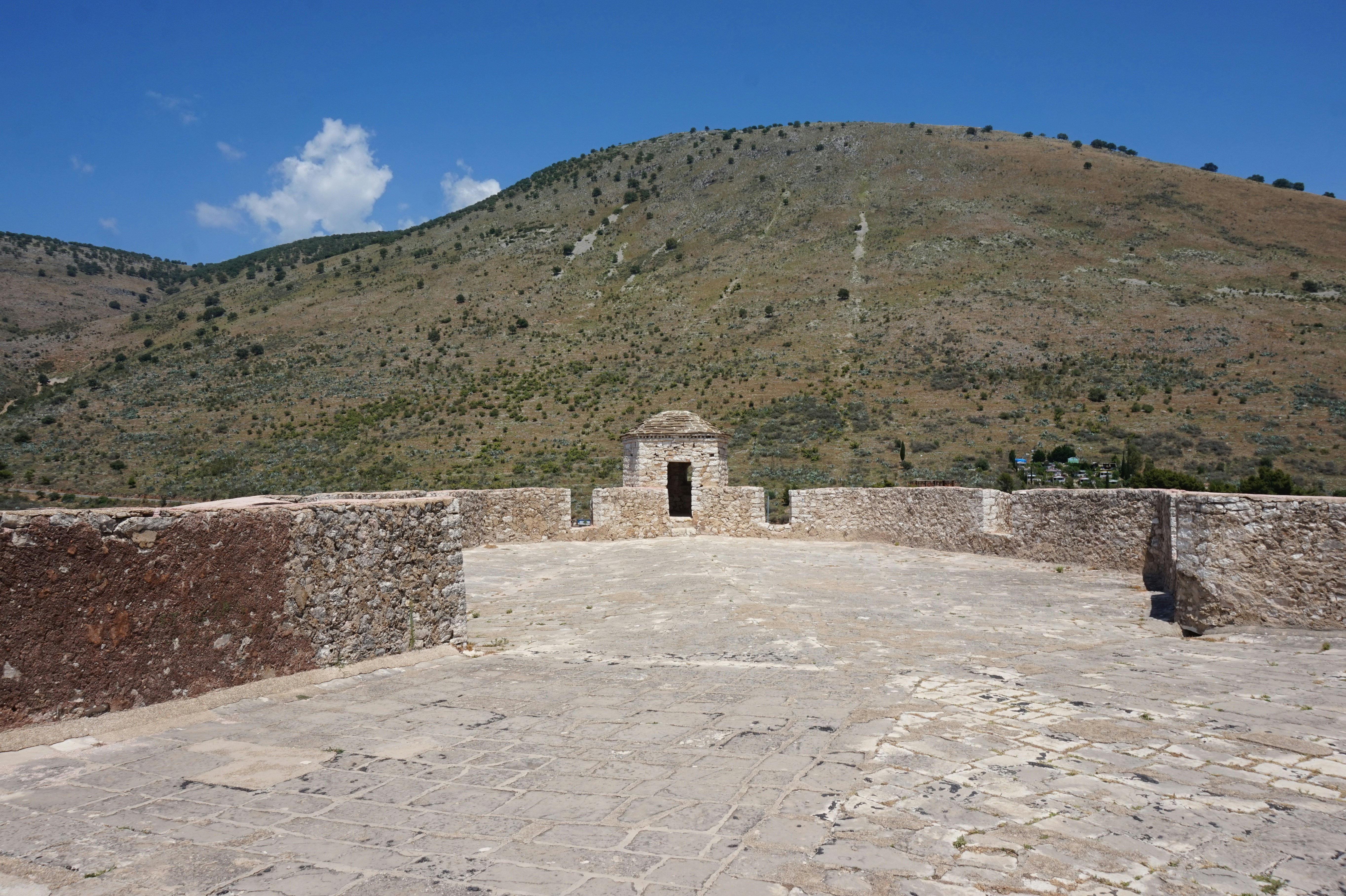 Hilltop Fortress Gateway: Sunlit Stone Courtyard Framed by Blue Sky