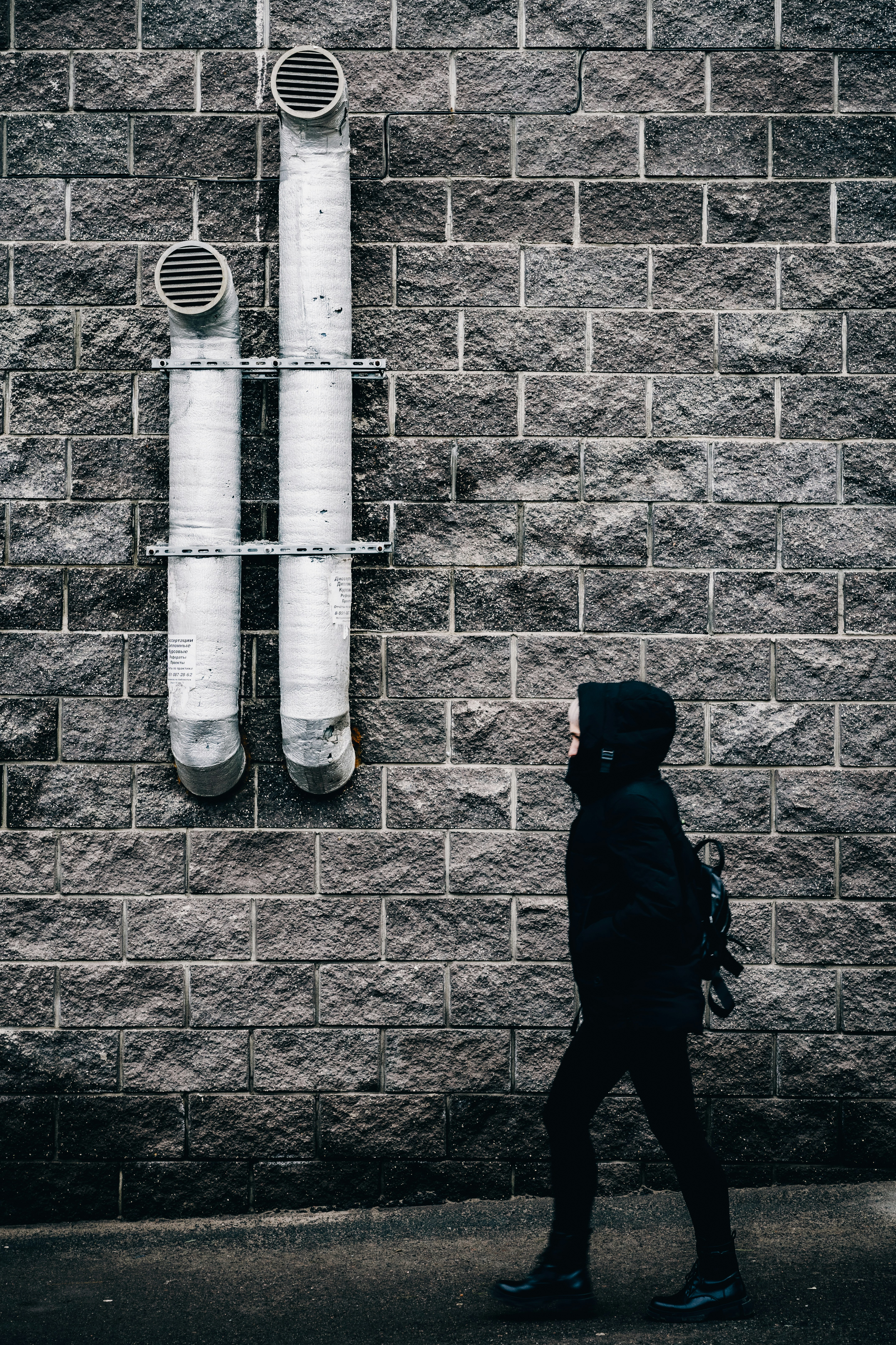 A person walking past a brick wall with pipes on it photo – Free City ...