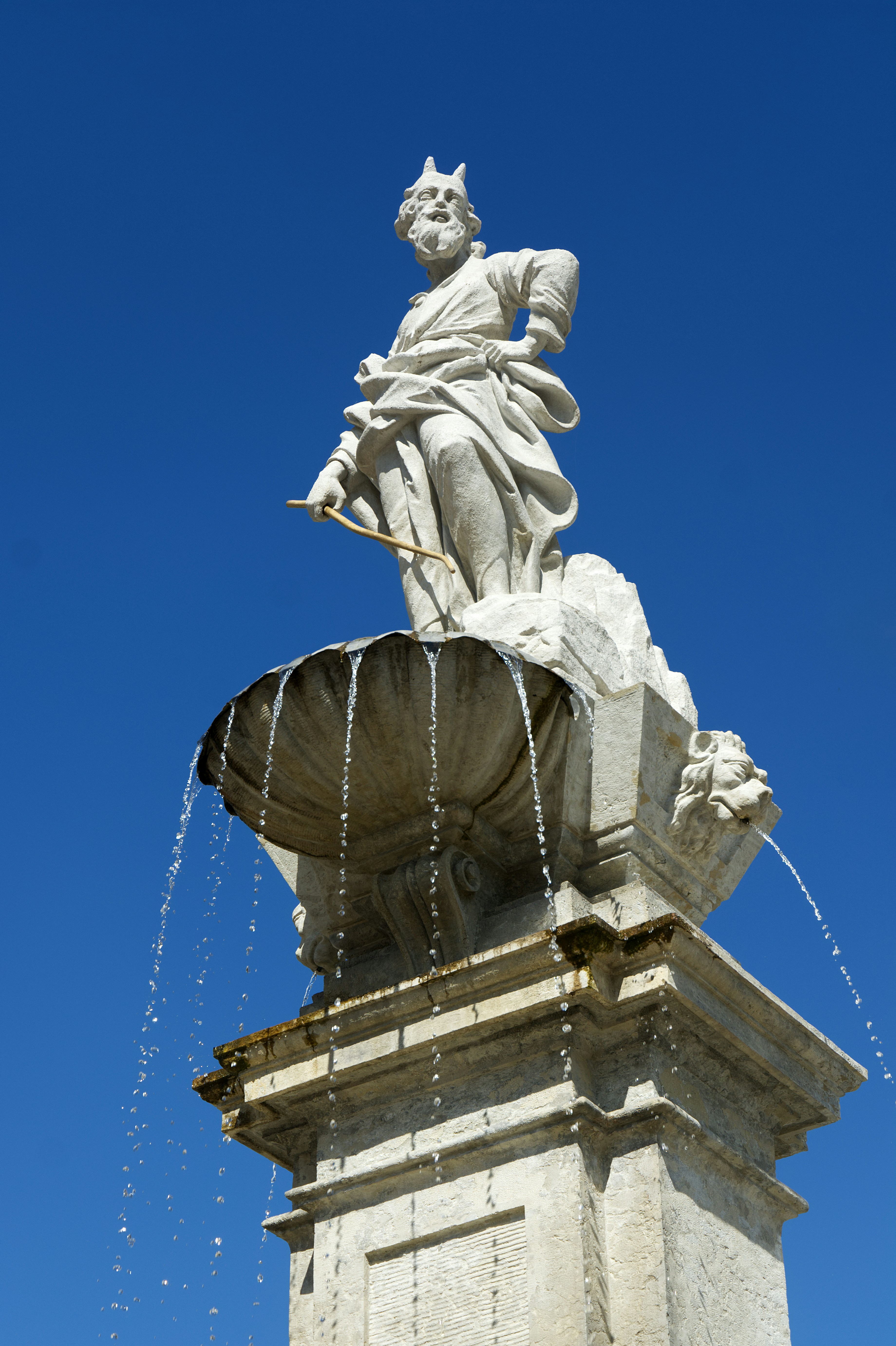 Marble Sentinel Over Water: A statue crowns a stone fountain beneath a cobalt sky