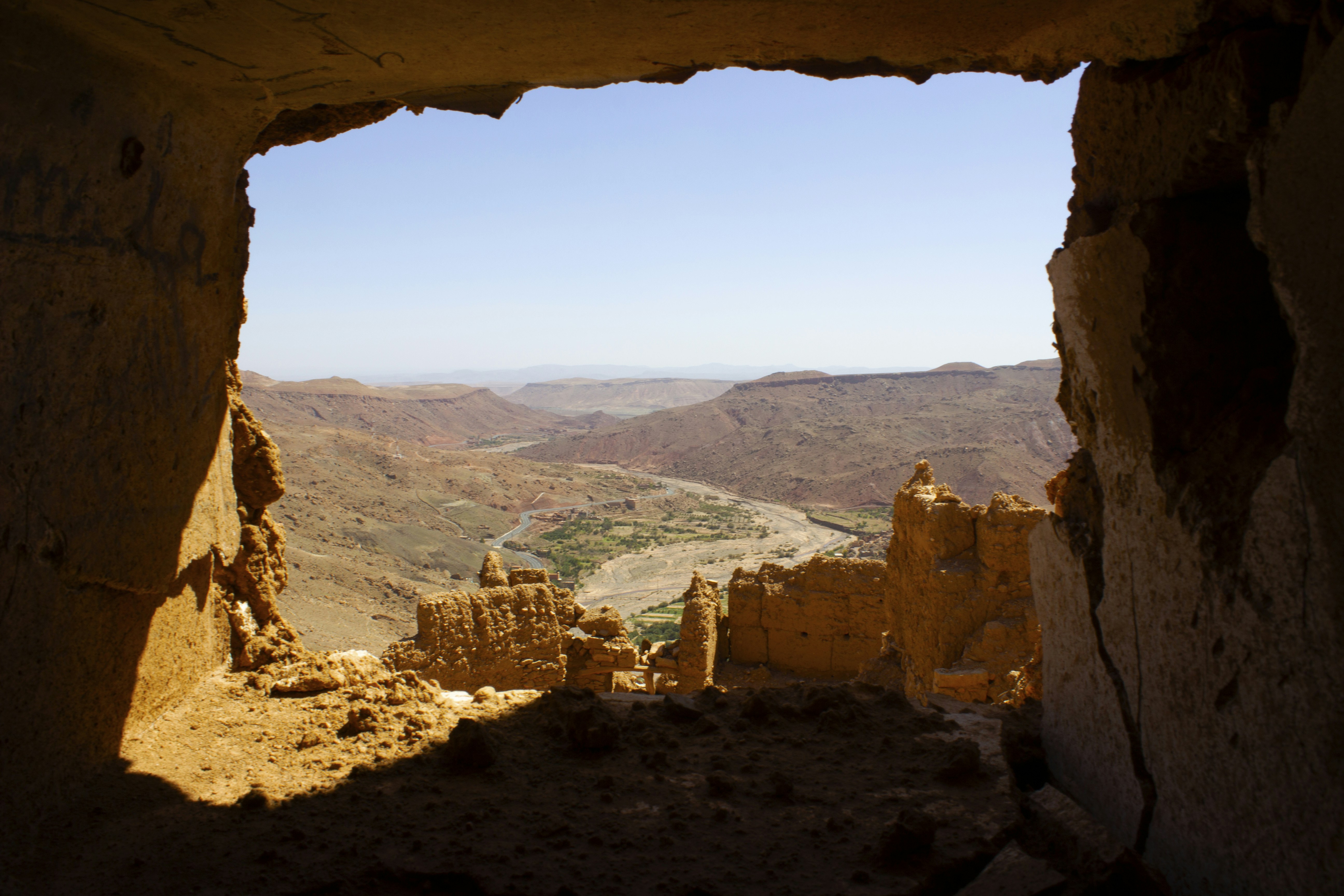 Desert valley viewed through the weathered frame of ancient ruins, with golden stone contrasting against a clear blue sky.