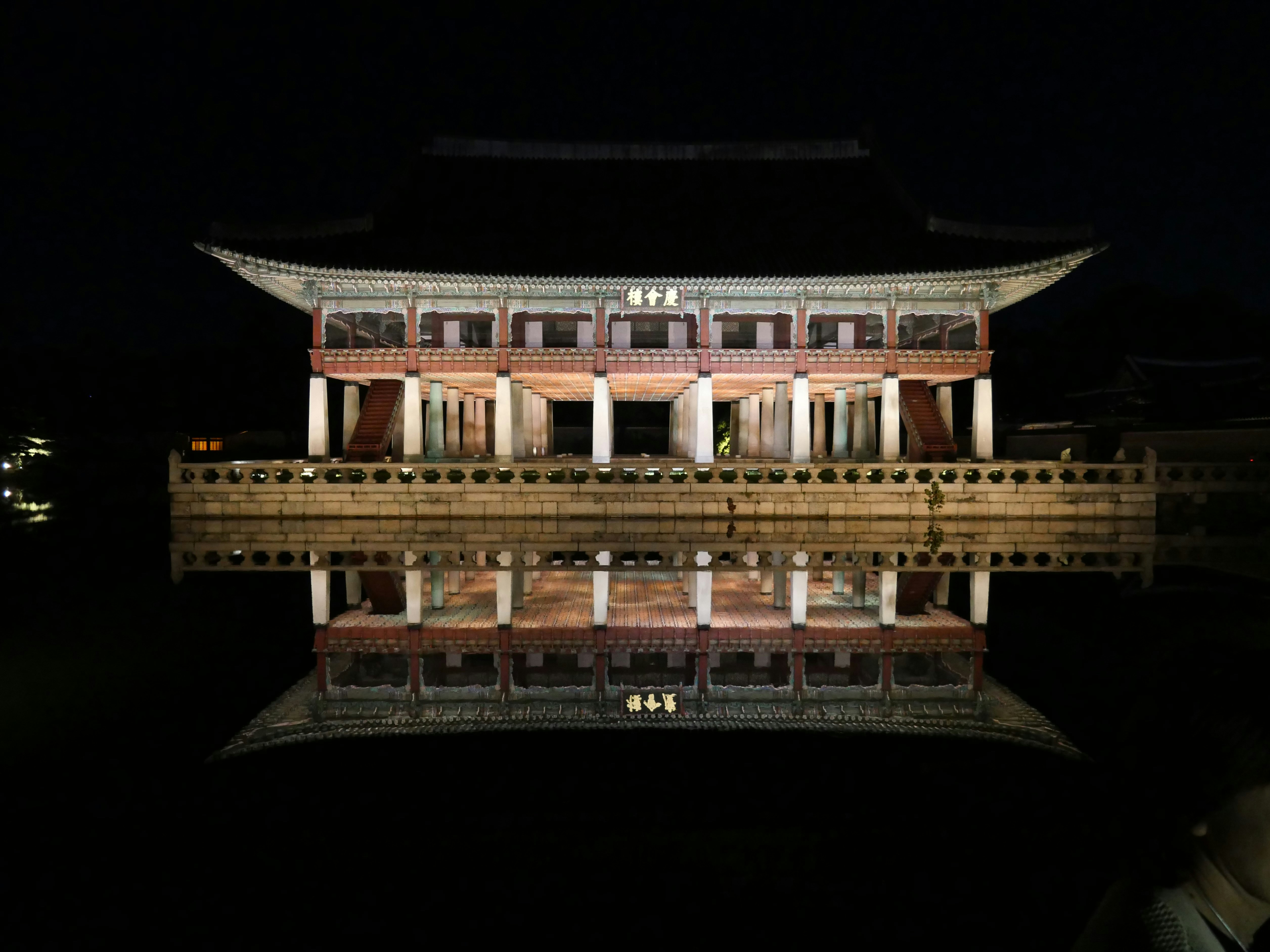 Traditional building aglow, reflecting perfectly in calm water, framed by the night.