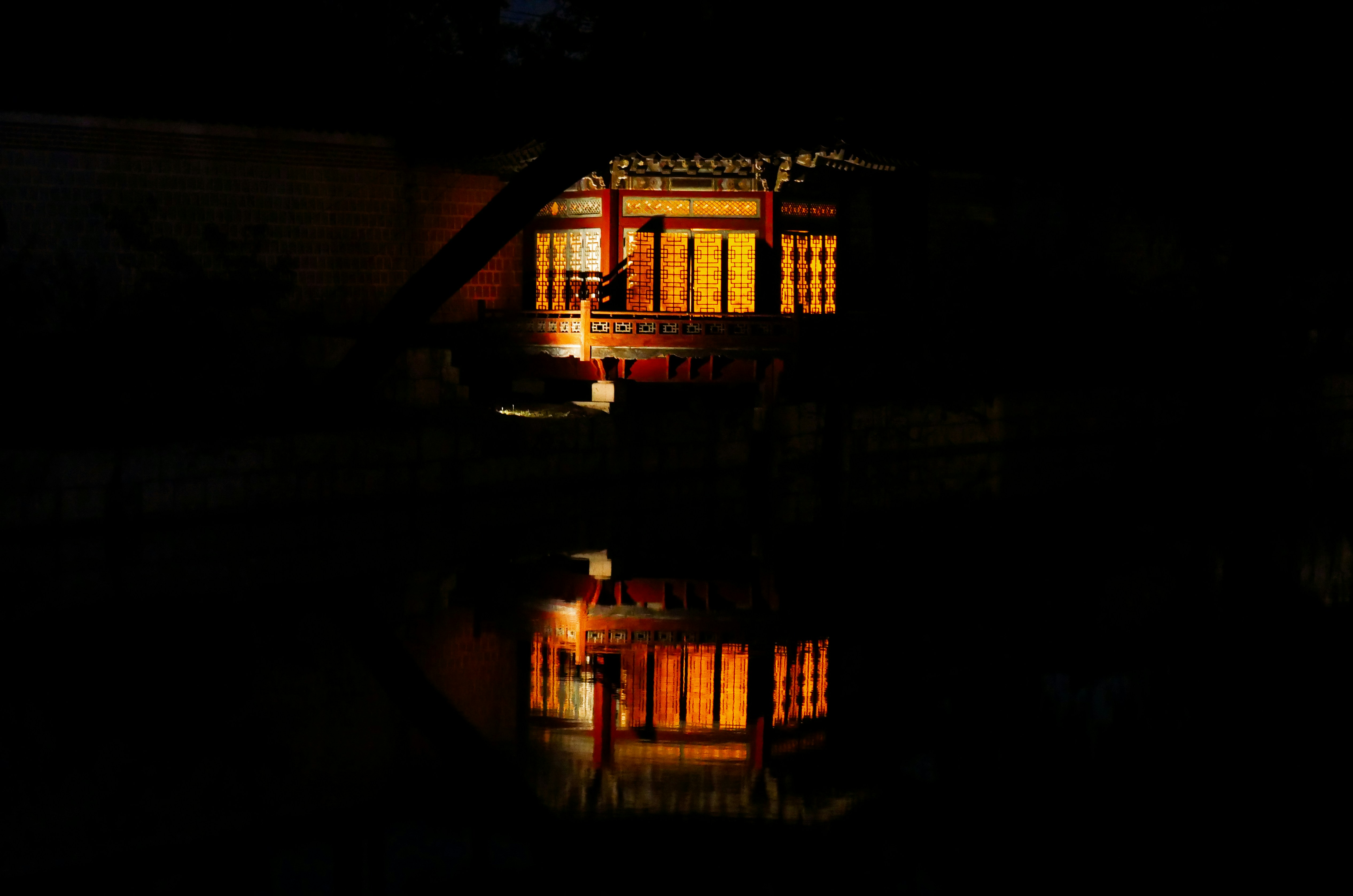 Traditional pavilion glowing warmly against the night, mirrored in calm water.