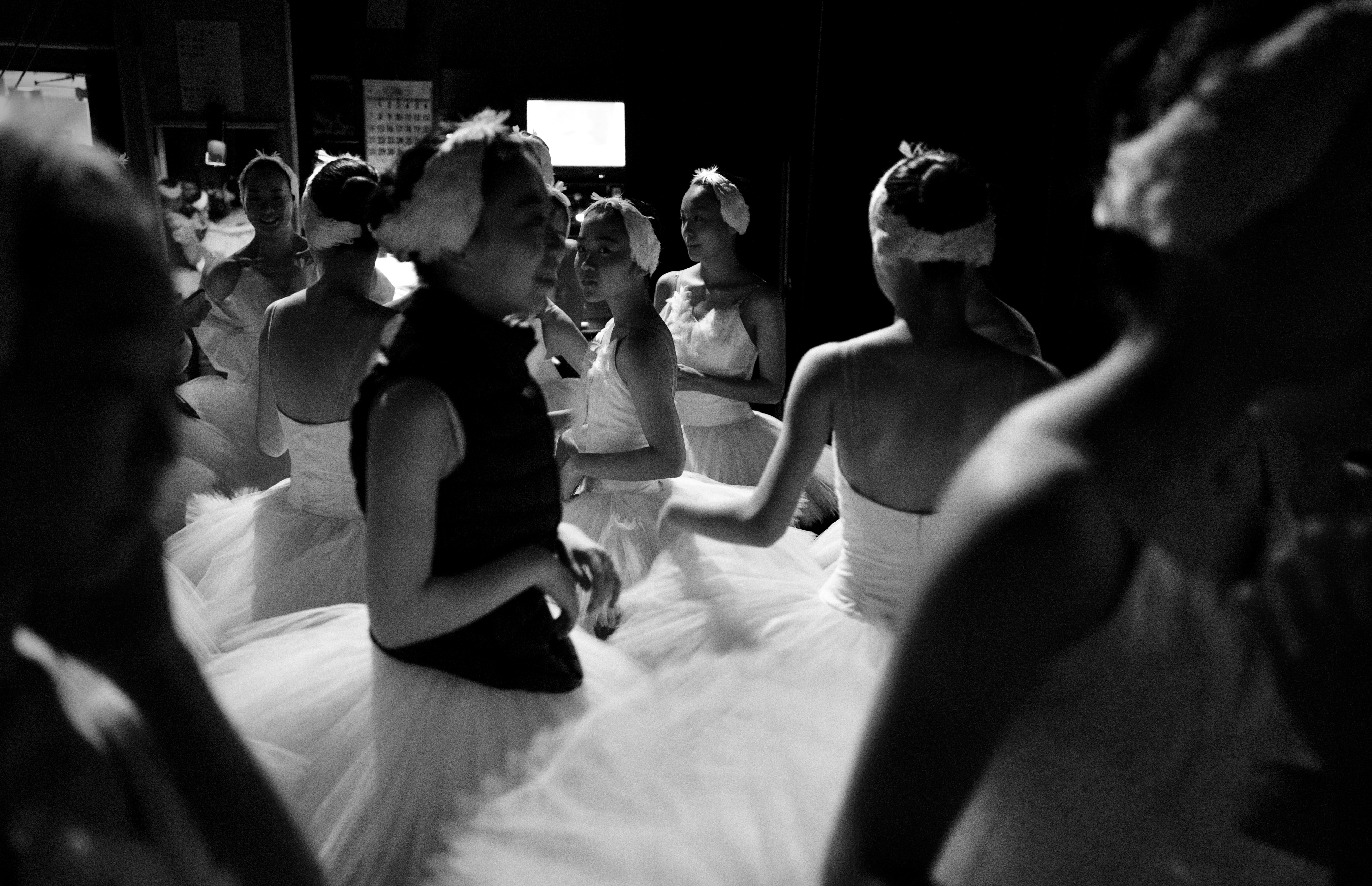 Ballet dancers in tutus gather backstage with soft lighting creating dramatic contrasts.