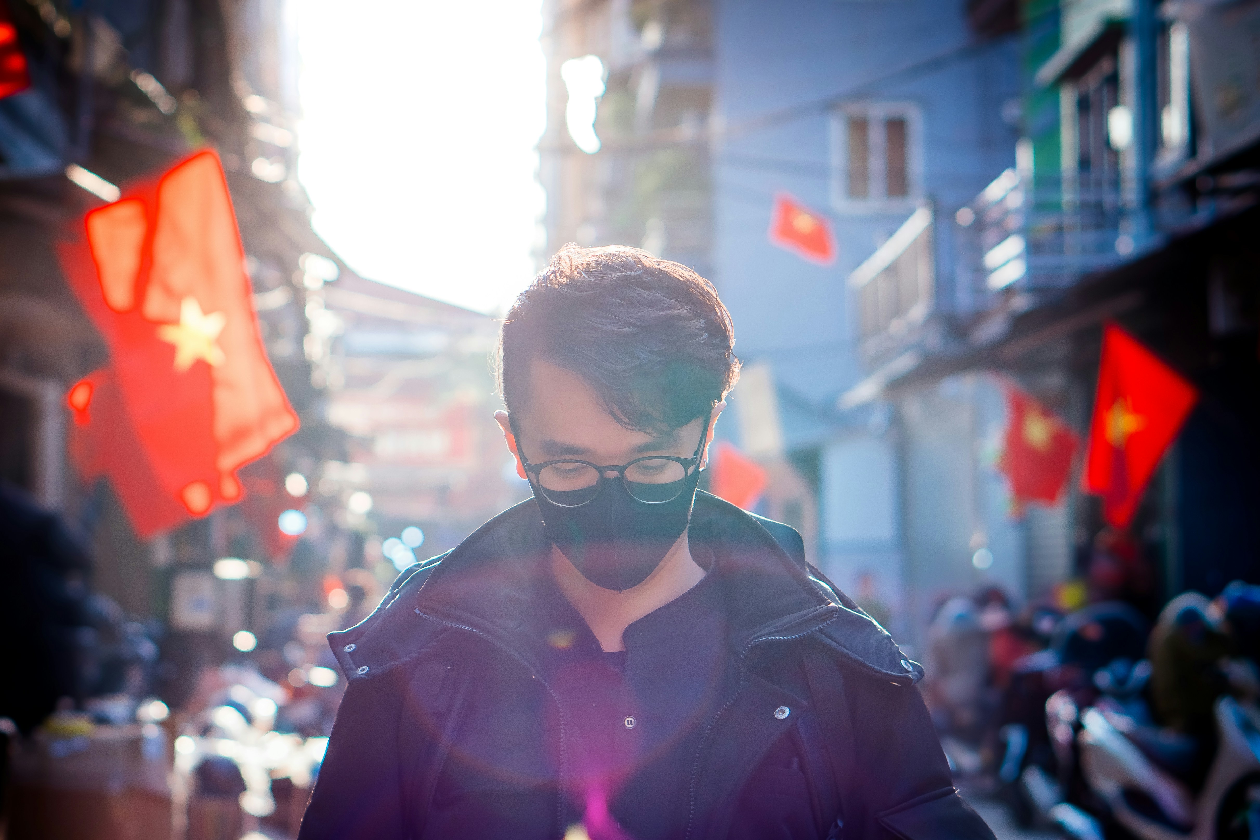 Haloed Amid Red Flags: A Masked Figure in a Sunlit Street