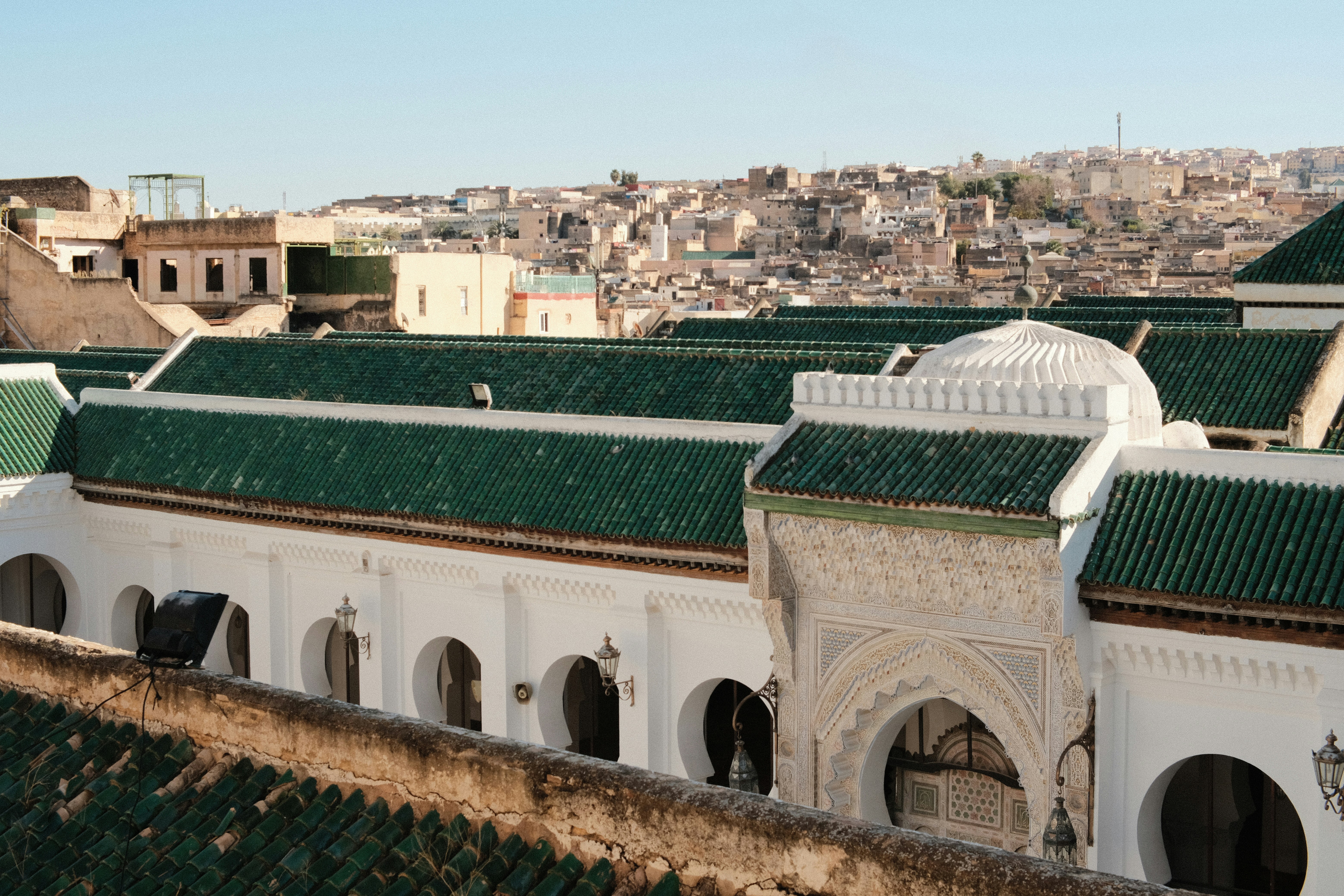 Green-tiled rooftops of Fez contrast with the sprawling urban landscape under a clear blue sky.