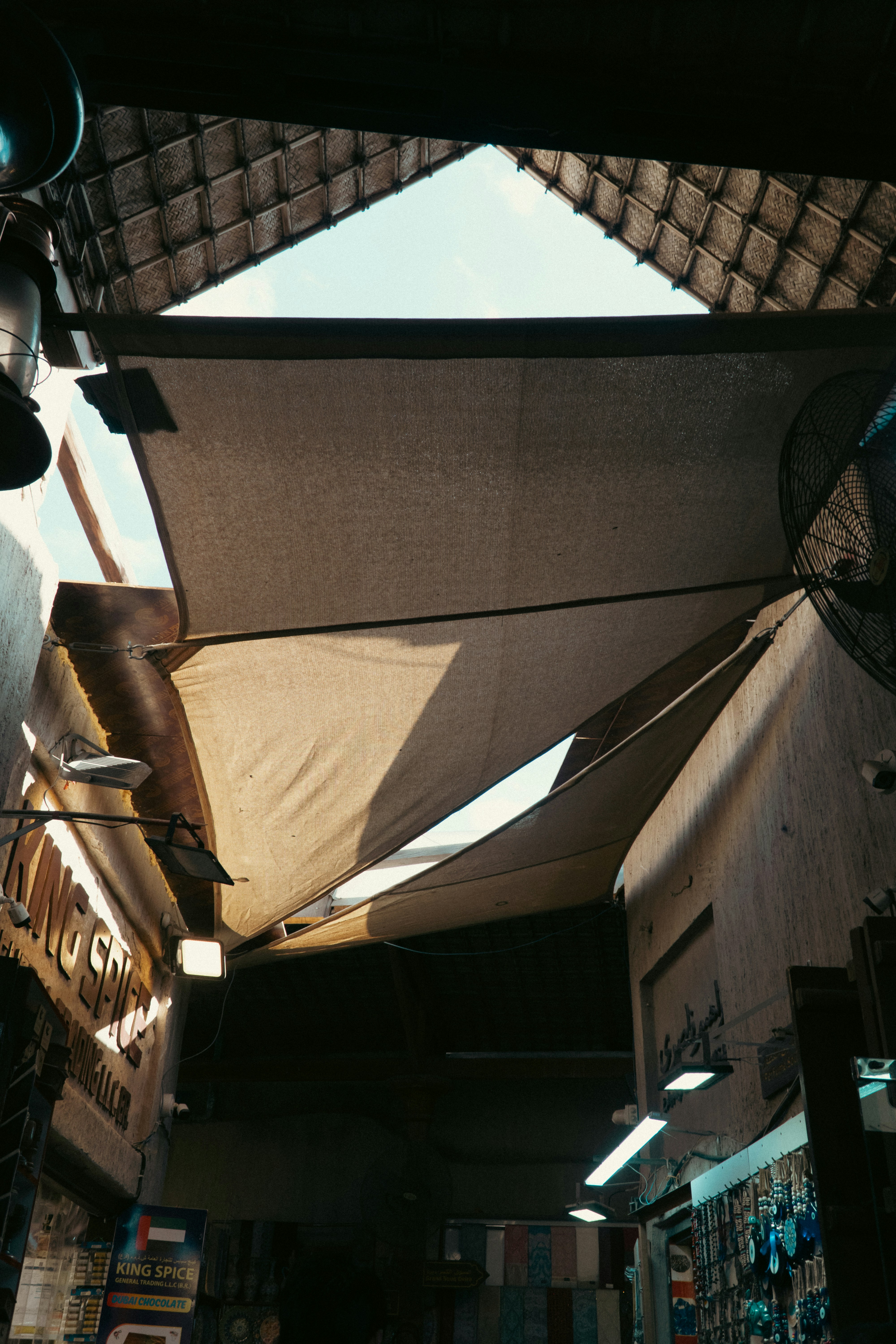 Sky Gap Over a Market Alley: Shade Sails Framing a Dim Passage