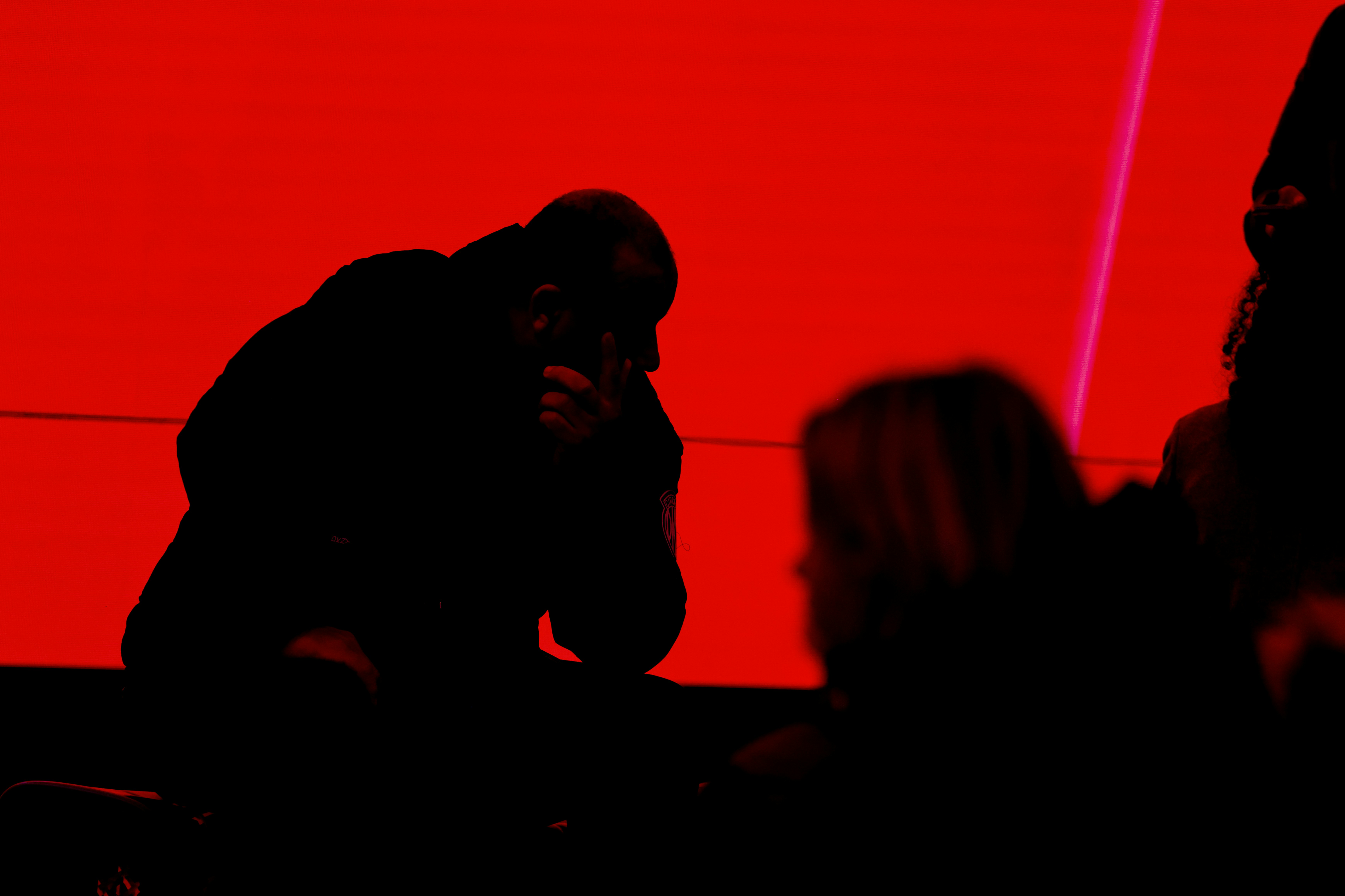 Silhouette of a person in a reflective pose against a vivid red background, highlighting the contrast between light and shadow.