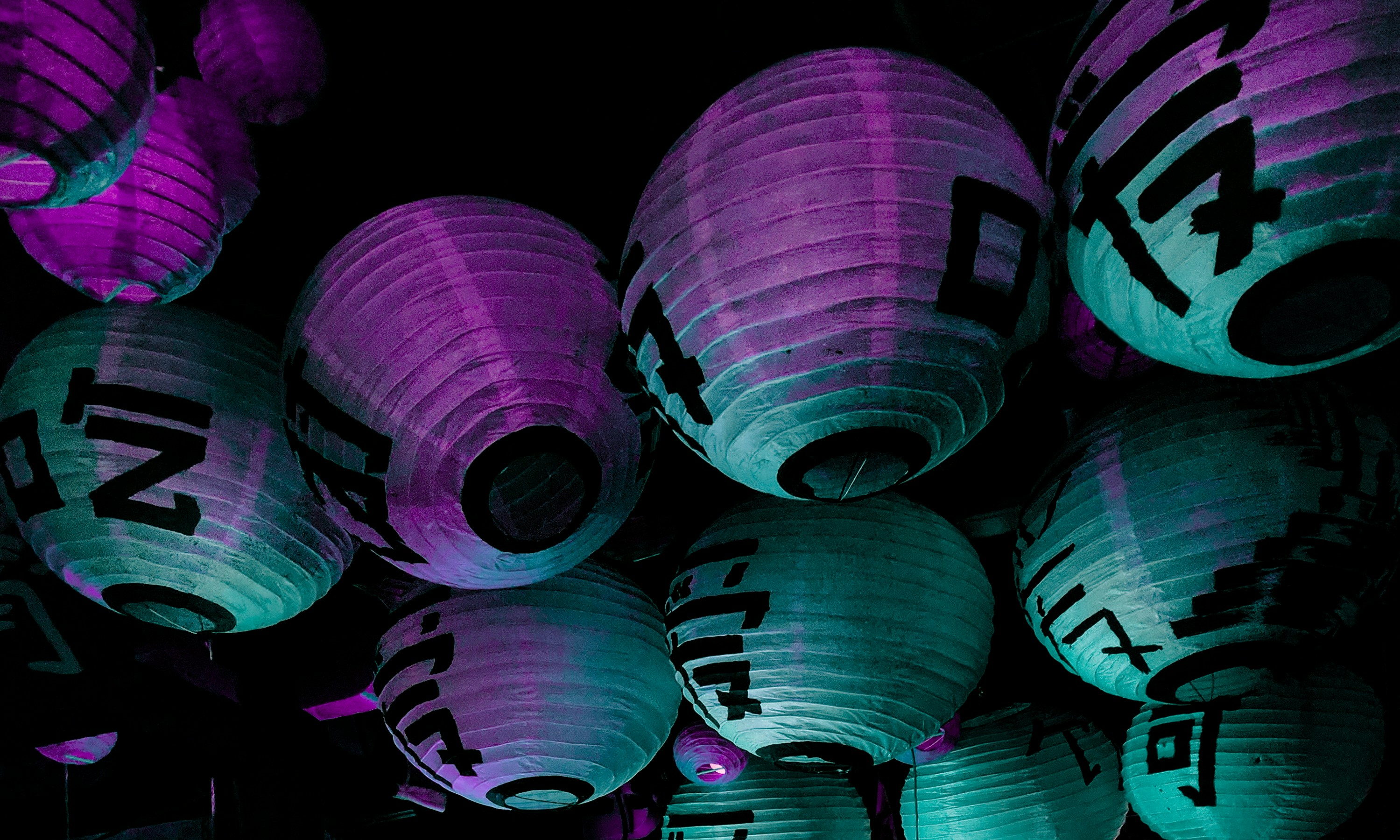 Colorful paper lanterns illuminated in shades of purple and teal against a dark background.