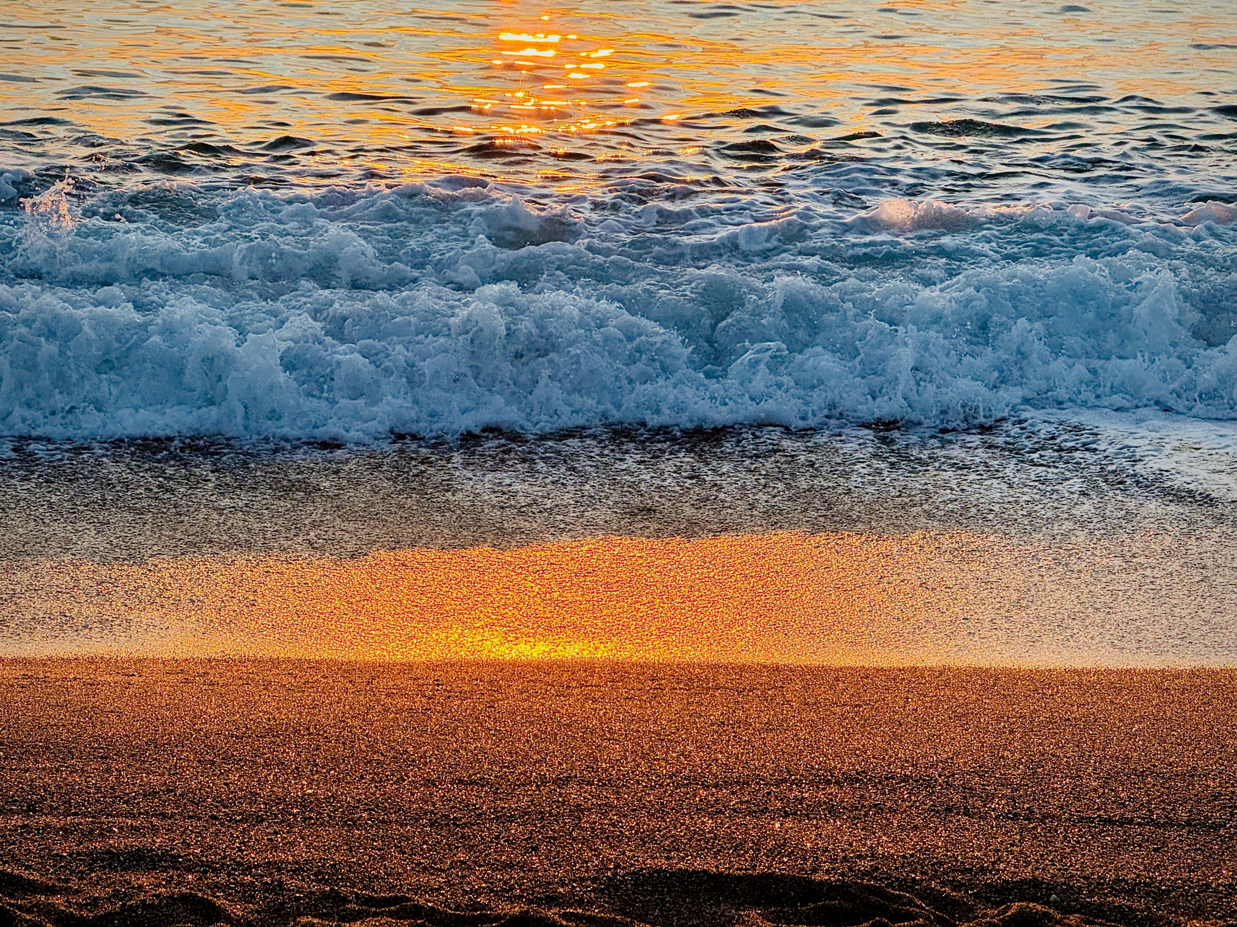 Gentle waves meet the sunlit shore with golden hues reflected on the water and sand.