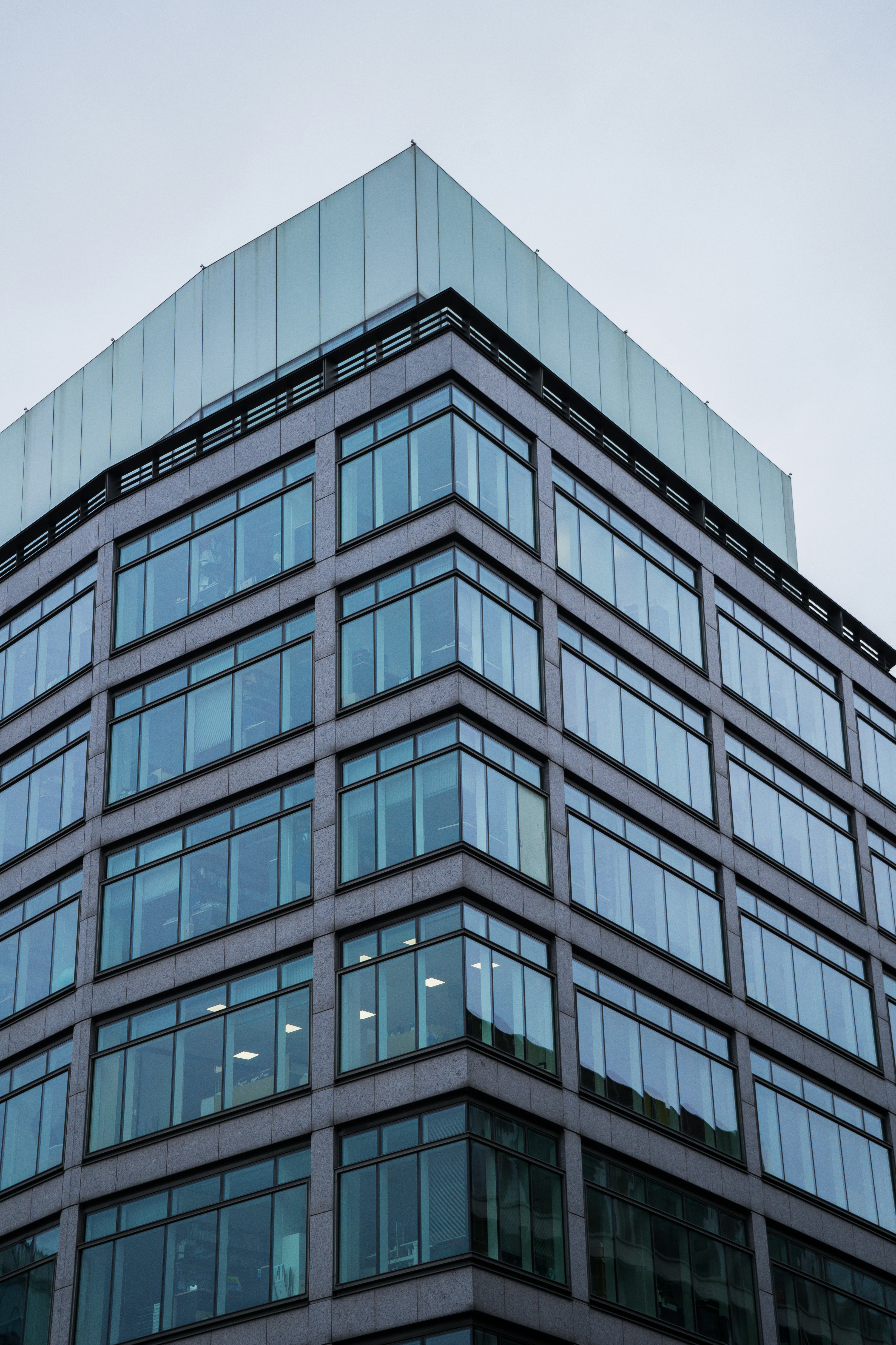 Angular glass facade of a contemporary office building, showcasing reflections and geometric patterns in a cloudy sky.