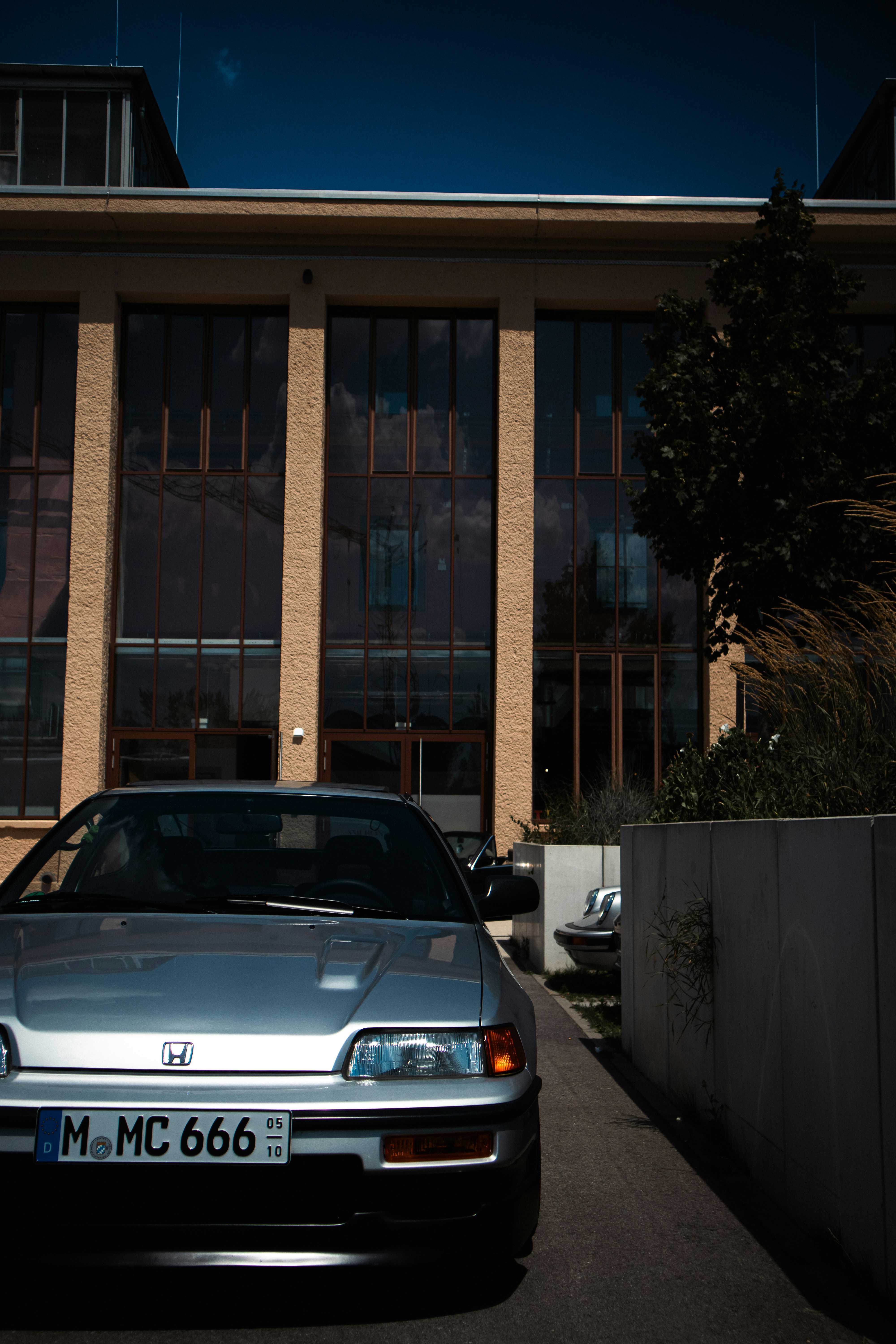 Classic silver car parked in front of a contemporary building under a clear blue sky.