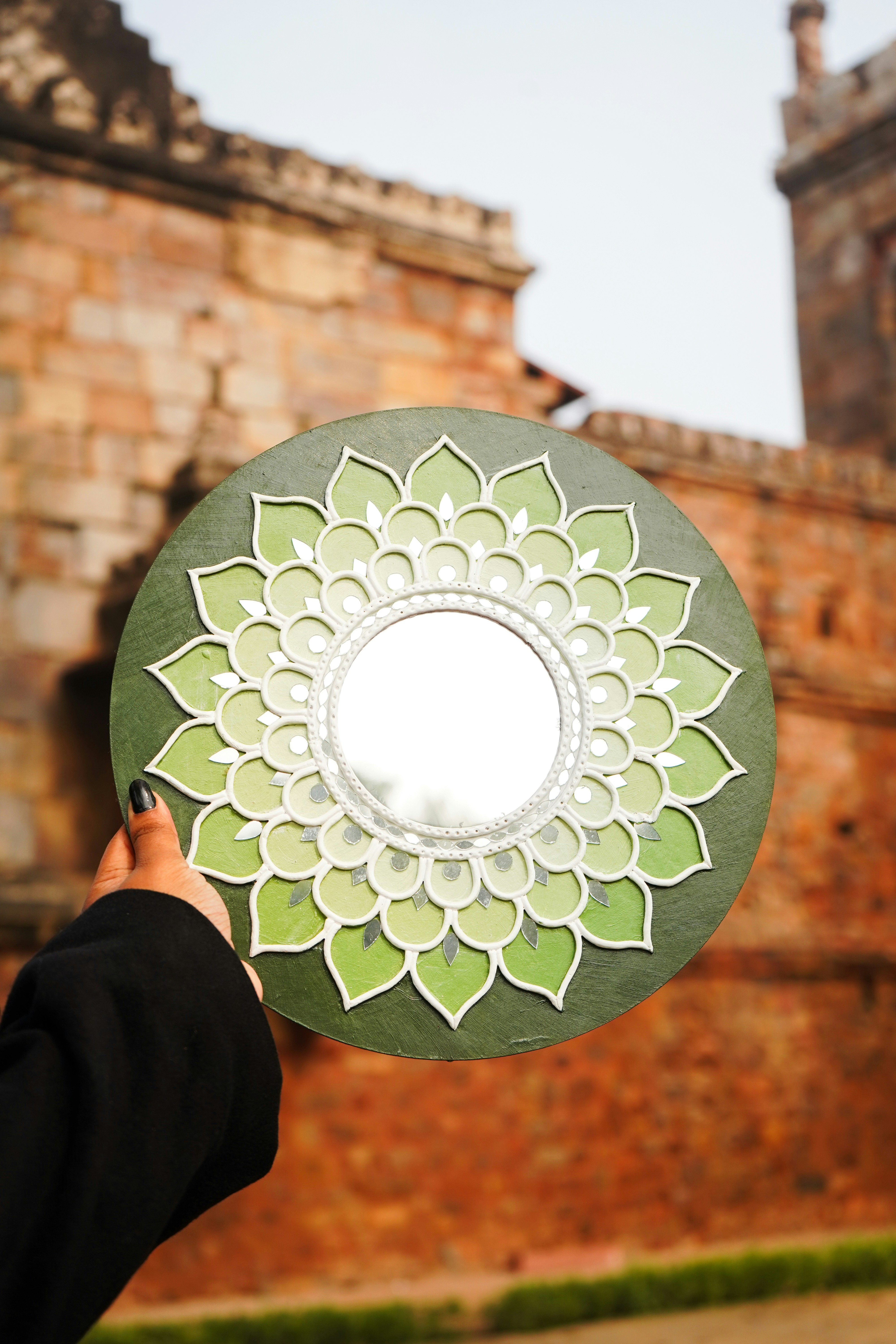 Circular mandala mirror held against historic brickwork