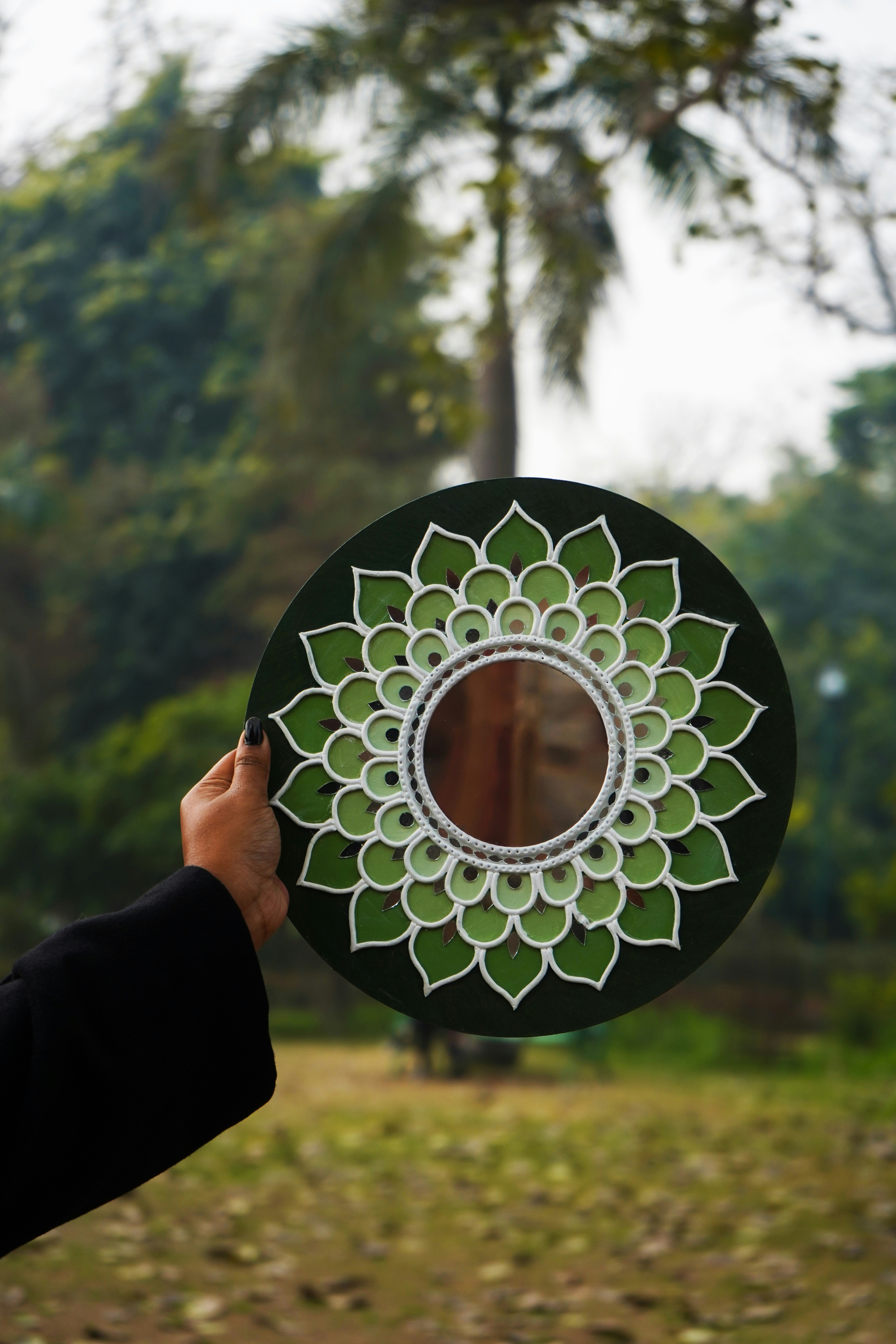 Green Mandala Mirror Held Against a Soft Park Backdrop