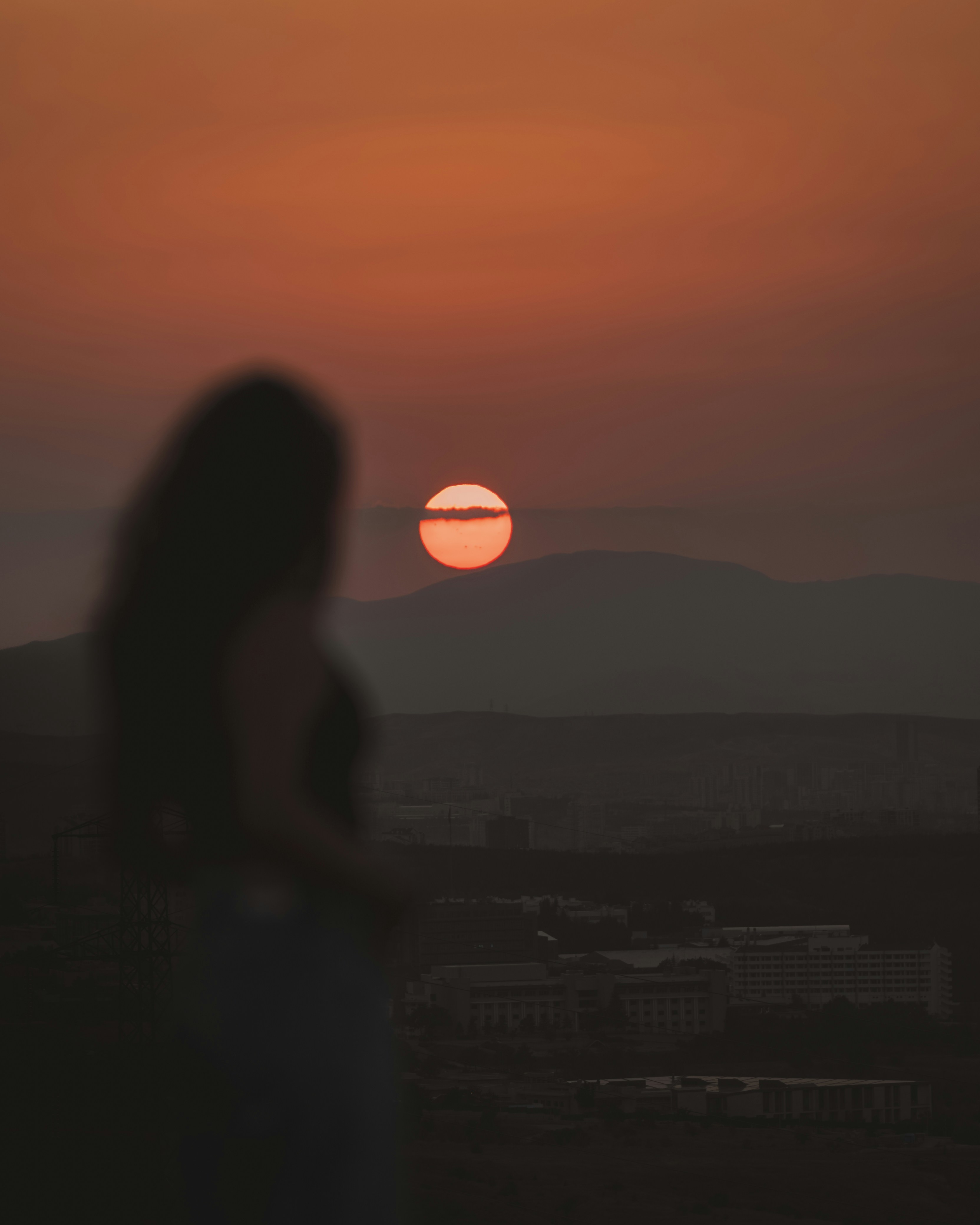 Horizon Ember: A Blurred Foreground Figure Framing Sunset Over a Quiet Cityscape