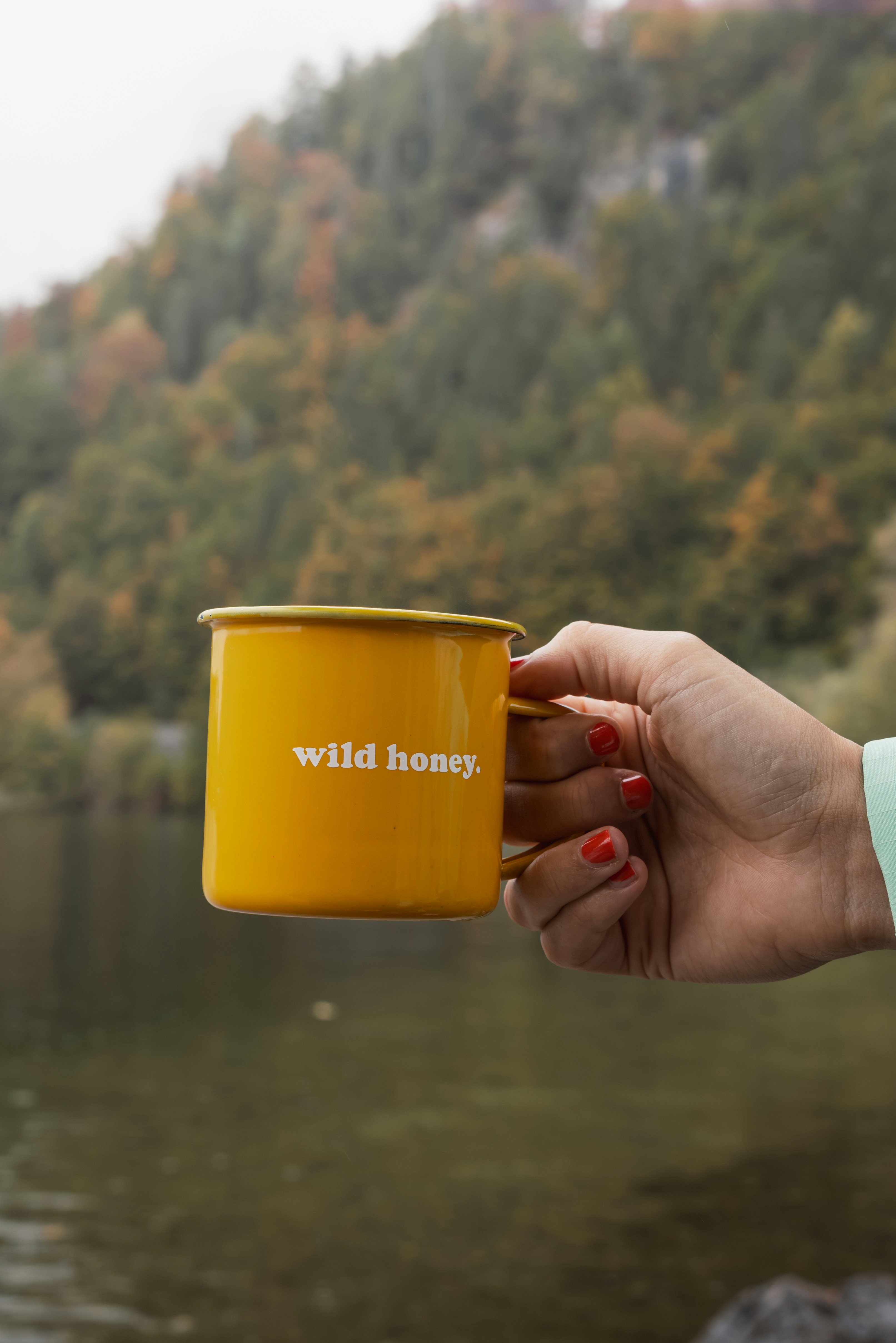 Amber Mug Over Calm Waters: A Handheld Moment Amid Fall Foliage