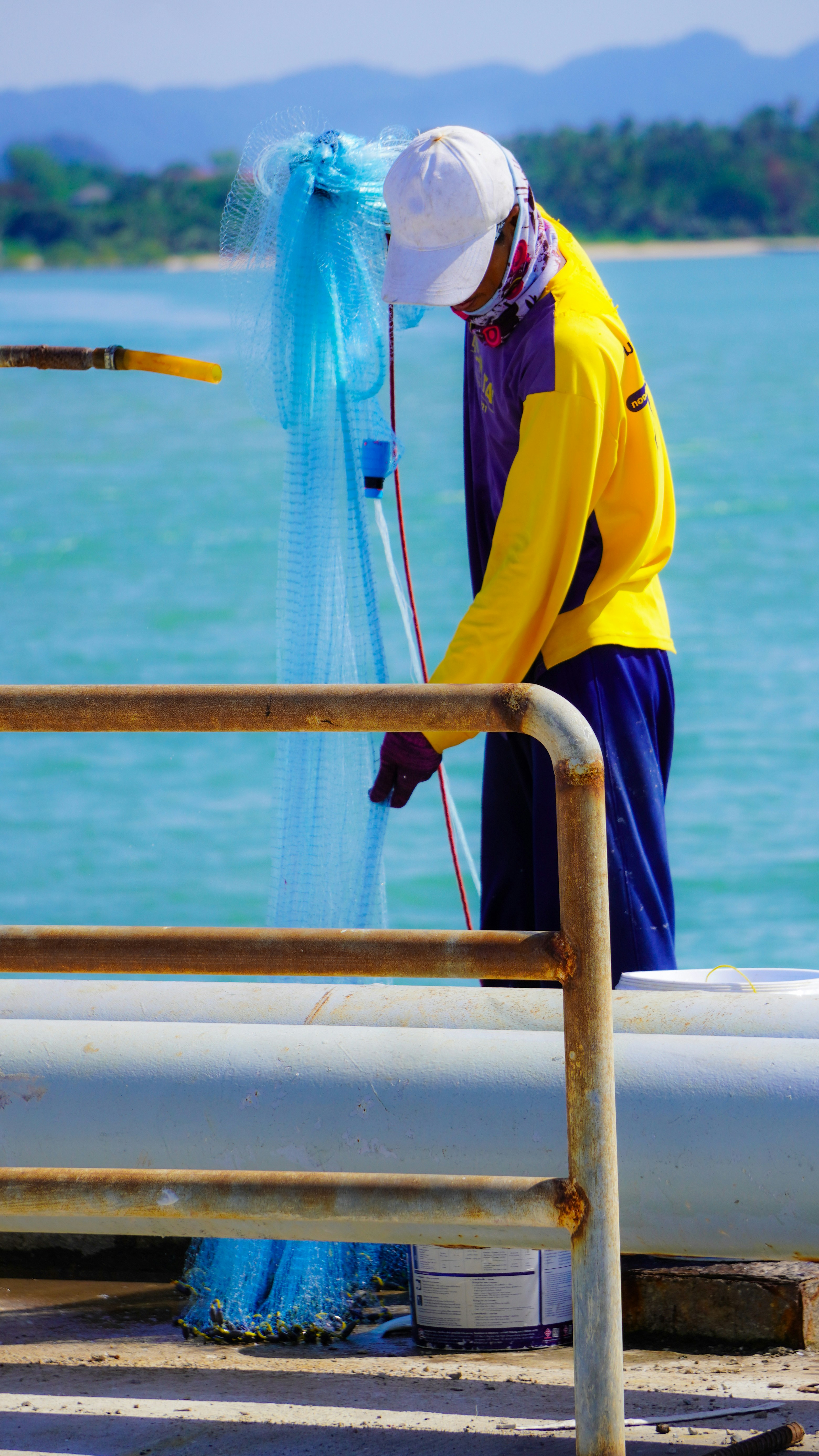 Blue Net by the Pier: A Fisherman's Quiet Task in Sunlit Turquoise Waters