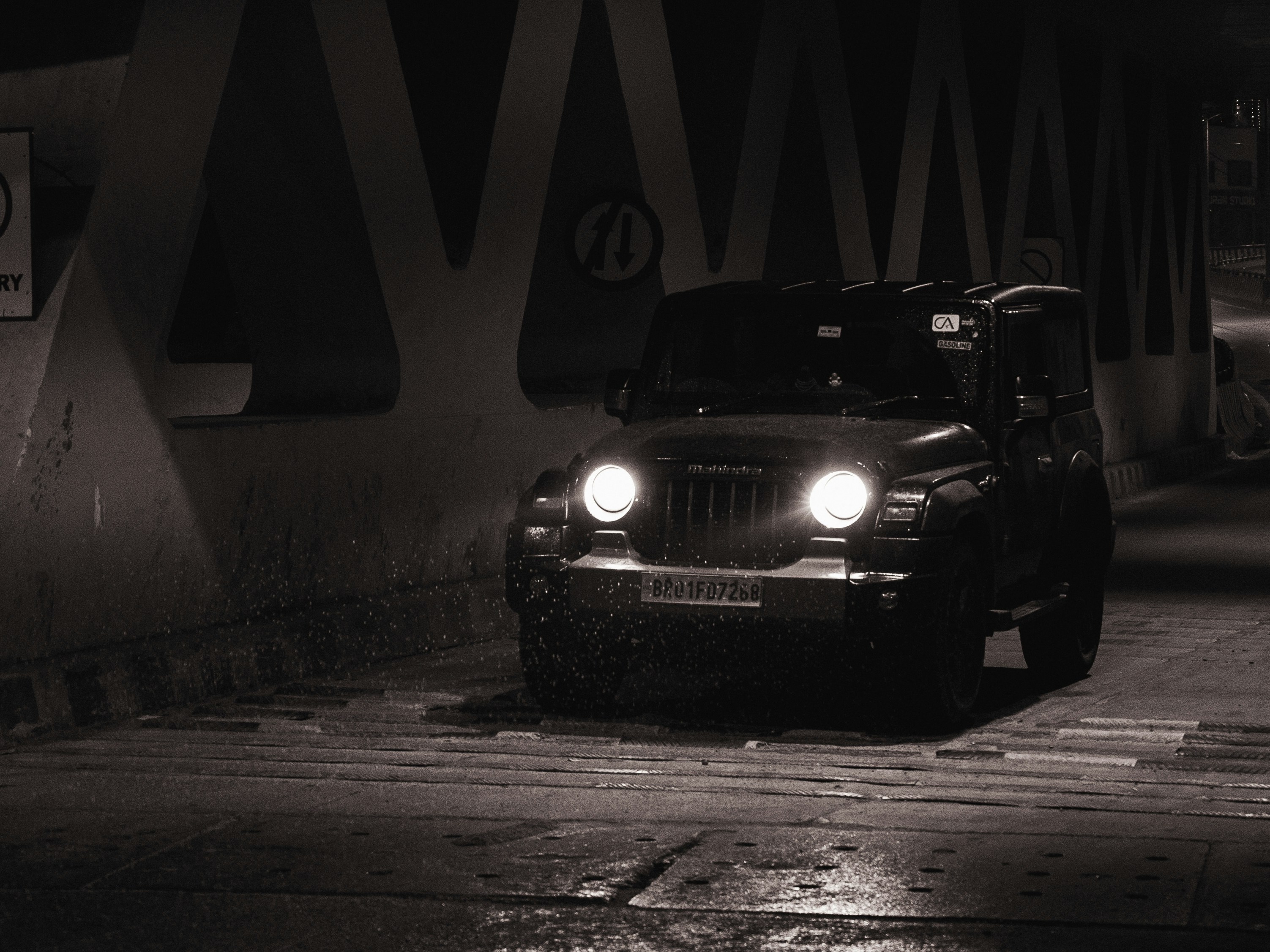 SUV with illuminated headlights emerges from an underpass, creating dramatic light contrasts on wet pavement.