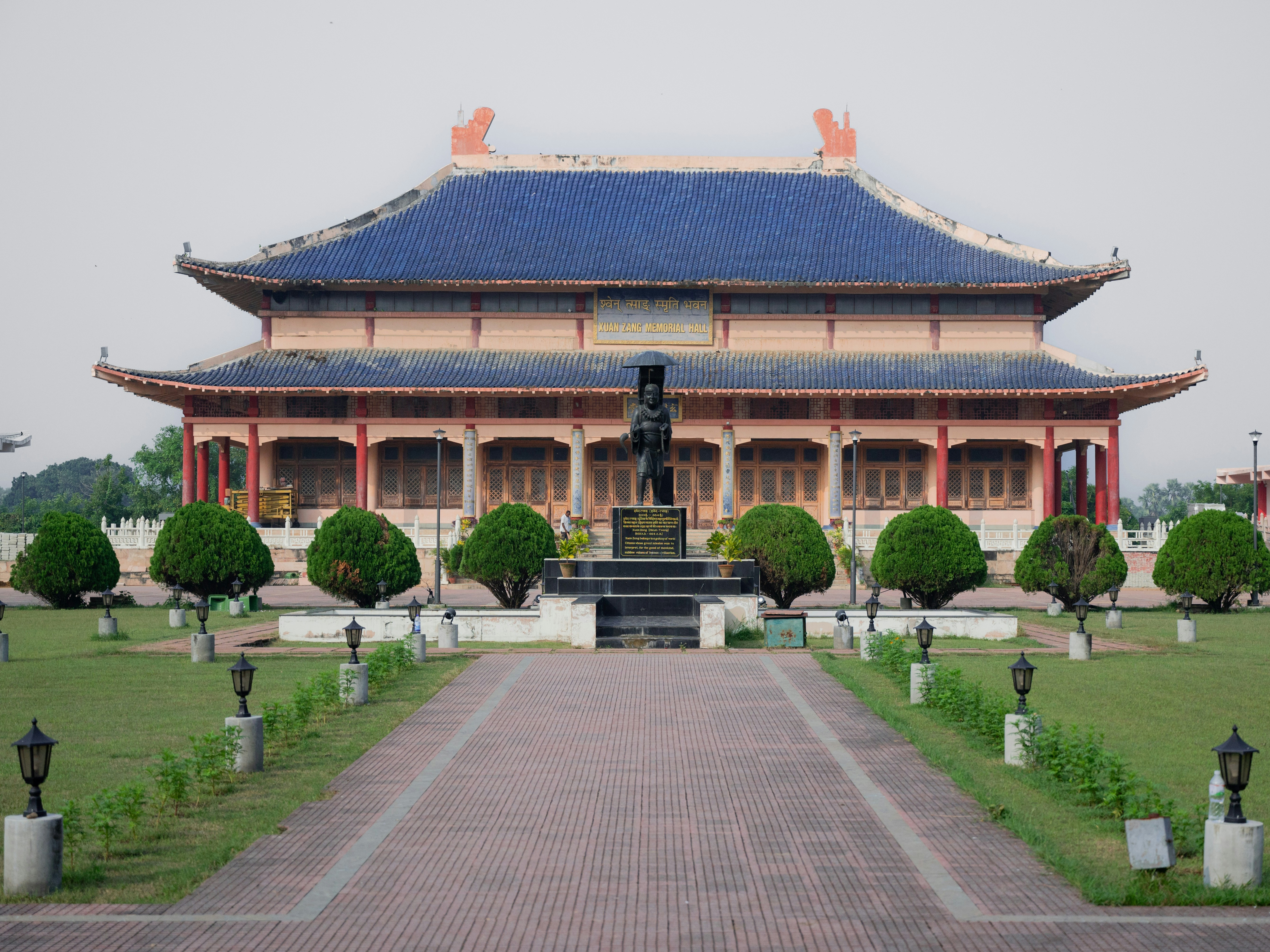A majestic traditional building with a blue tiled roof and intricate details, framed by manicured greenery and a statue at its base.