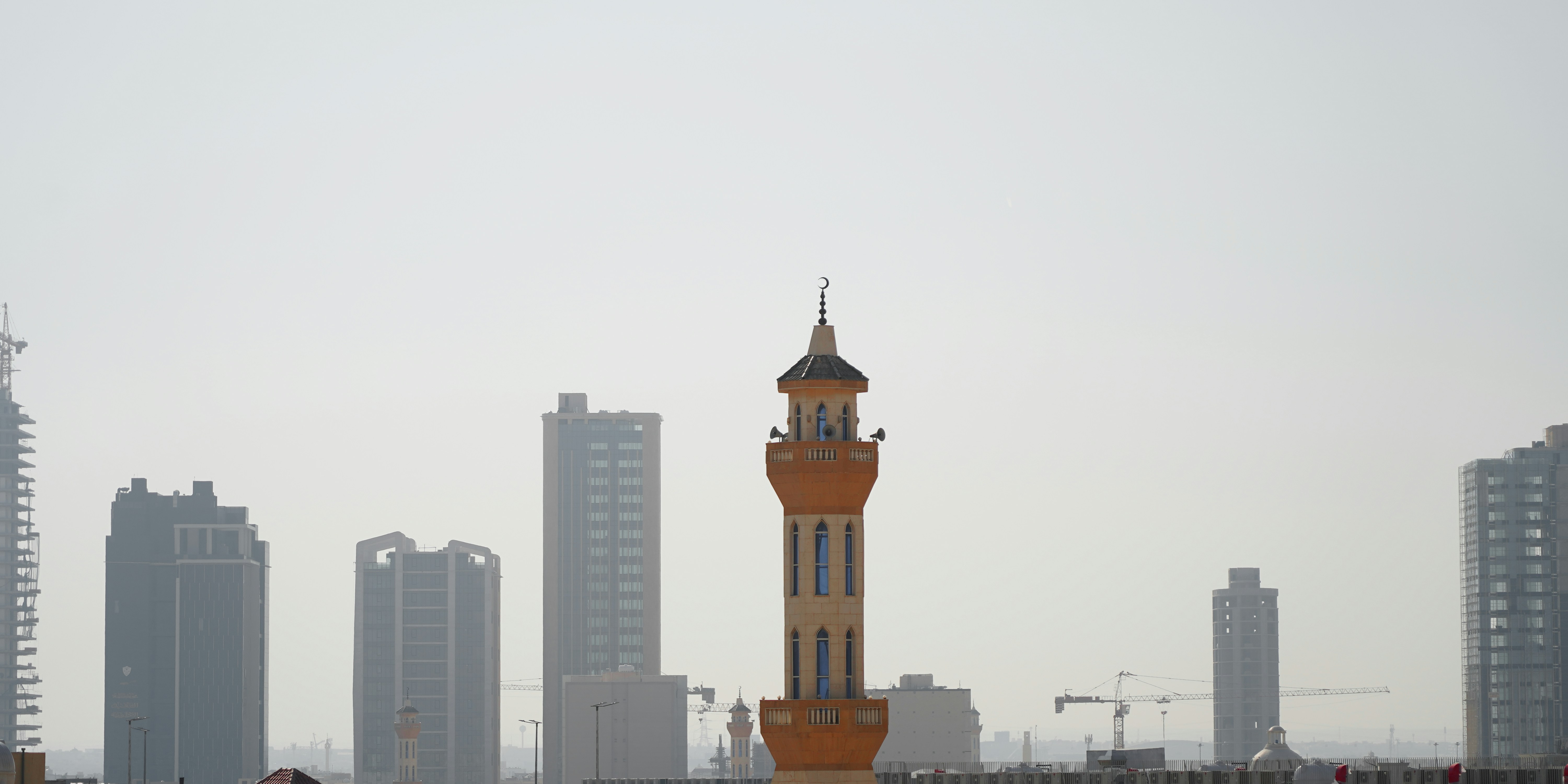 Traditional mosque tower contrasts with modern skyscrapers under a hazy sky.