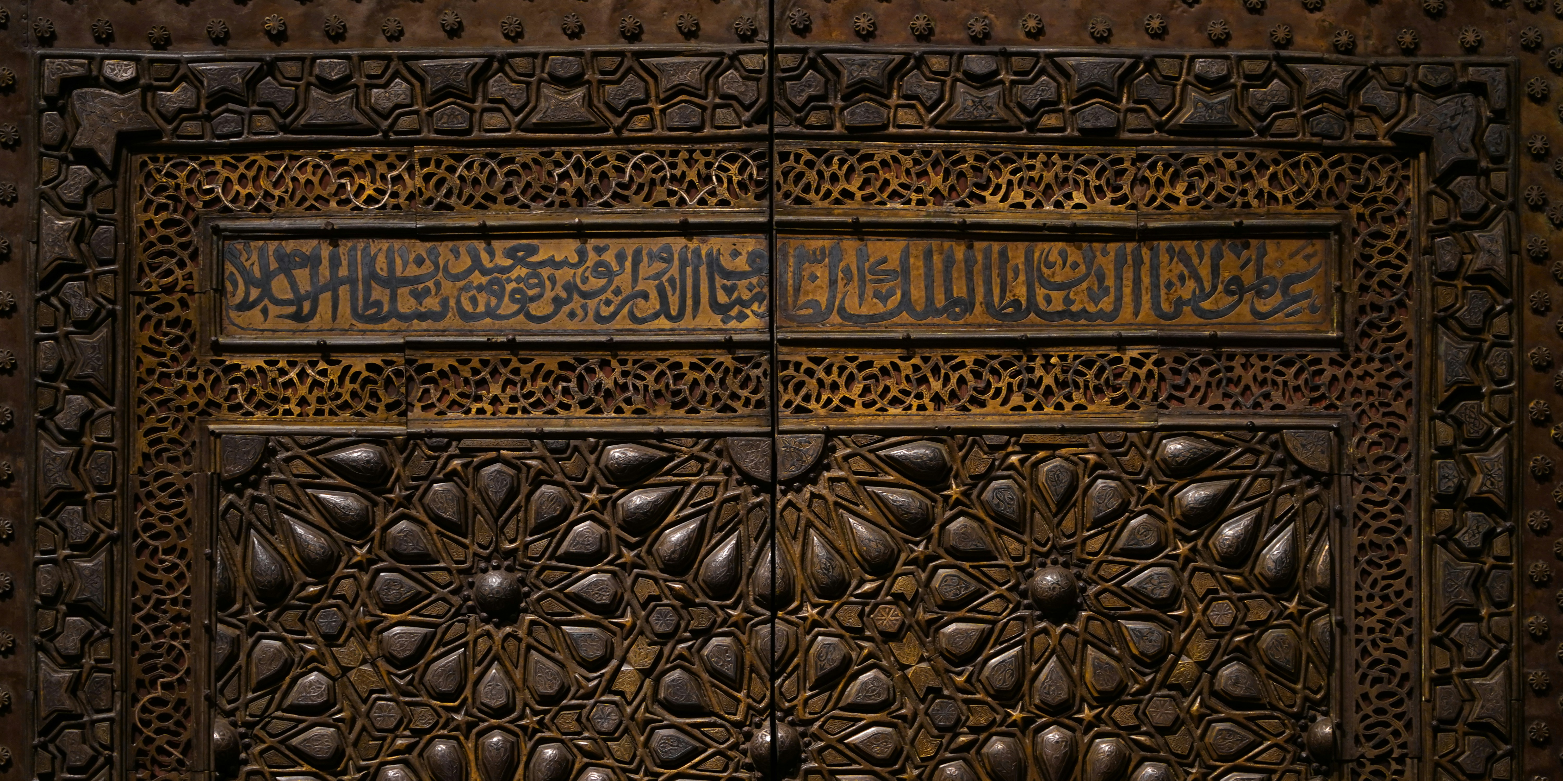Iron Script in Shadow: Close-Up of Floral Embossing and Arabic Calligraphy on a Metal Door