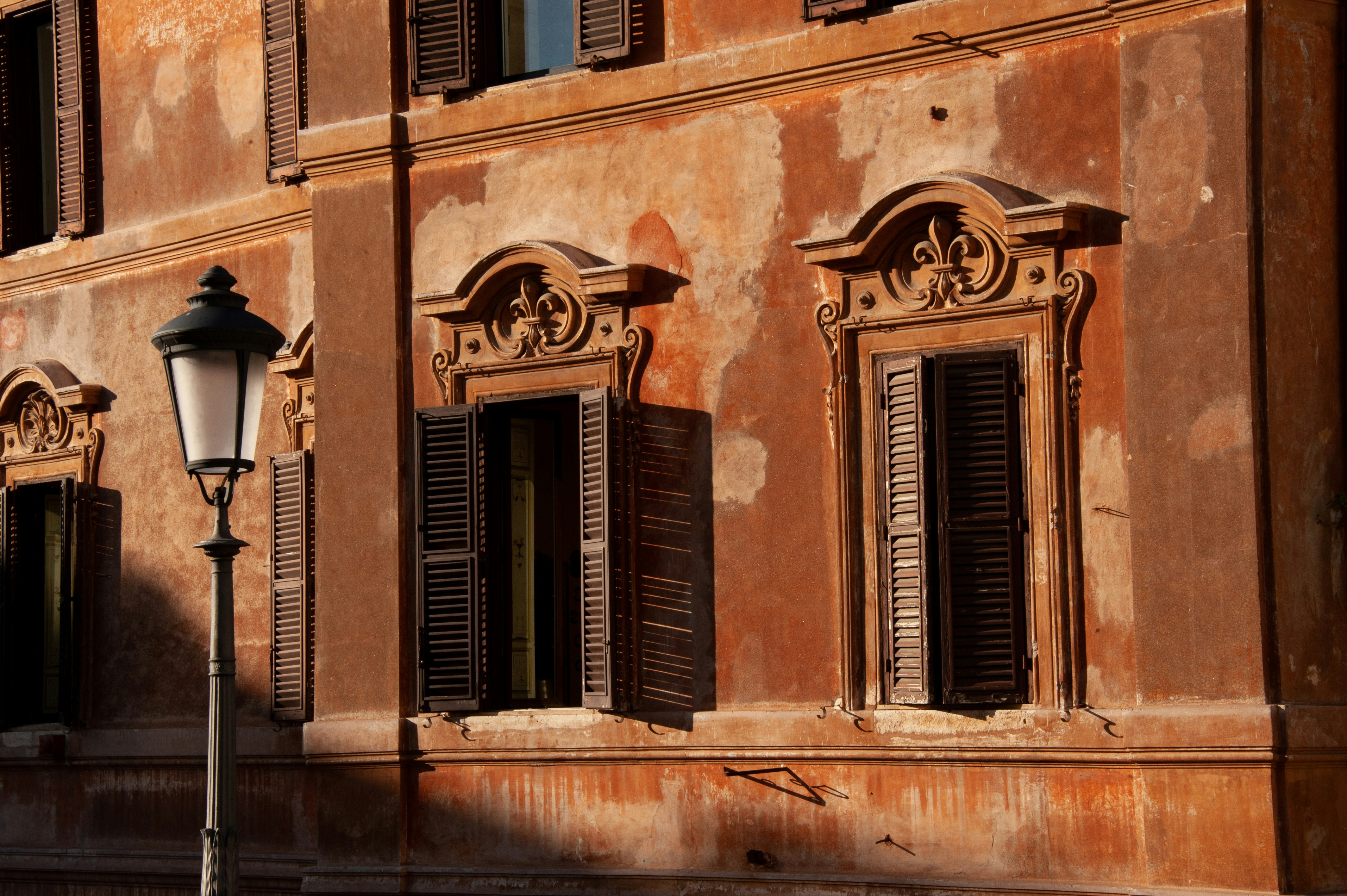 Sunlight casting shadows on a weathered building with ornate windows and a vintage street lamp.