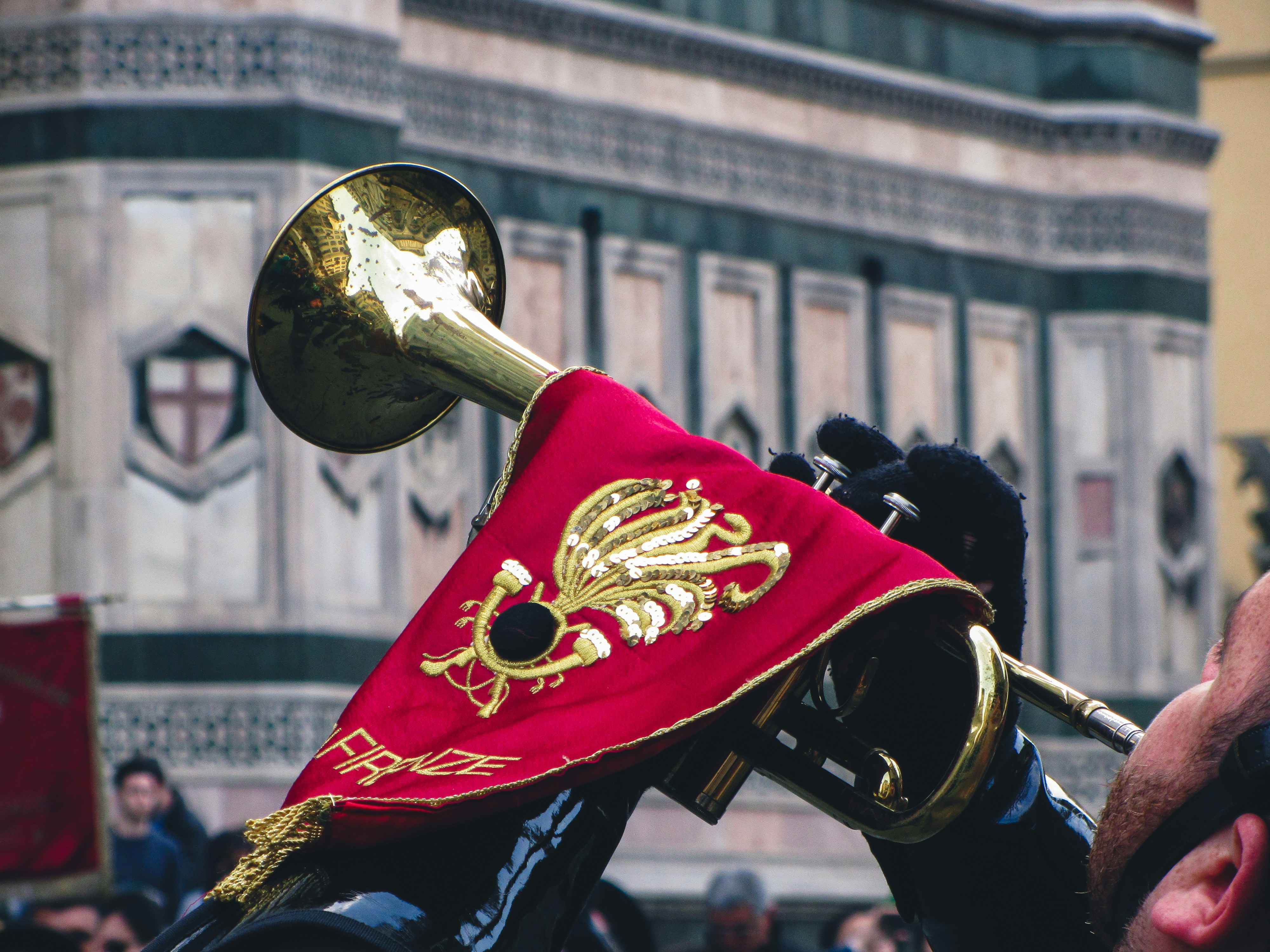 Brass trumpet with an ornate red banner against a historic European building.