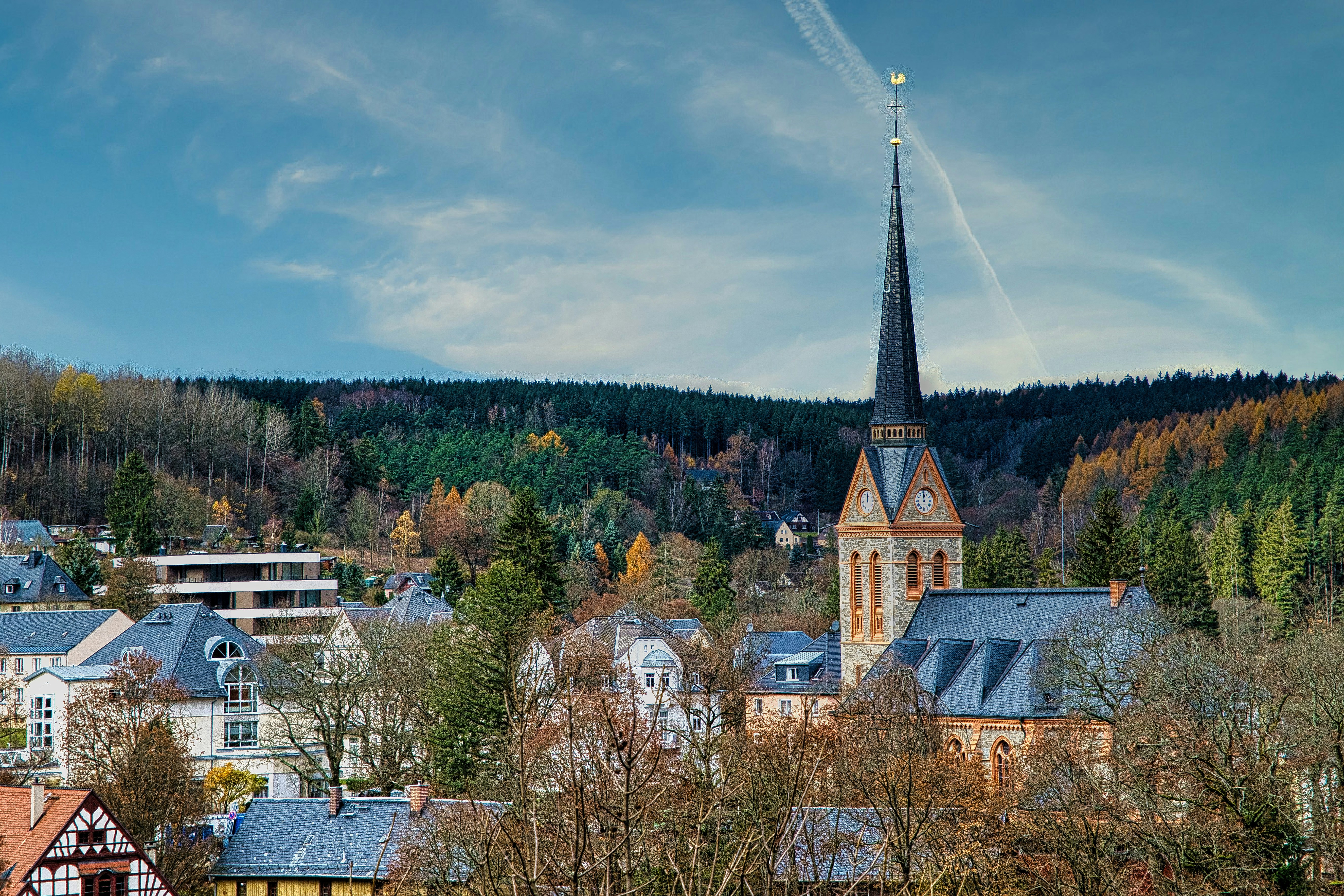 Village landscape with a prominent church steeple surrounded by autumn trees and distant hills.