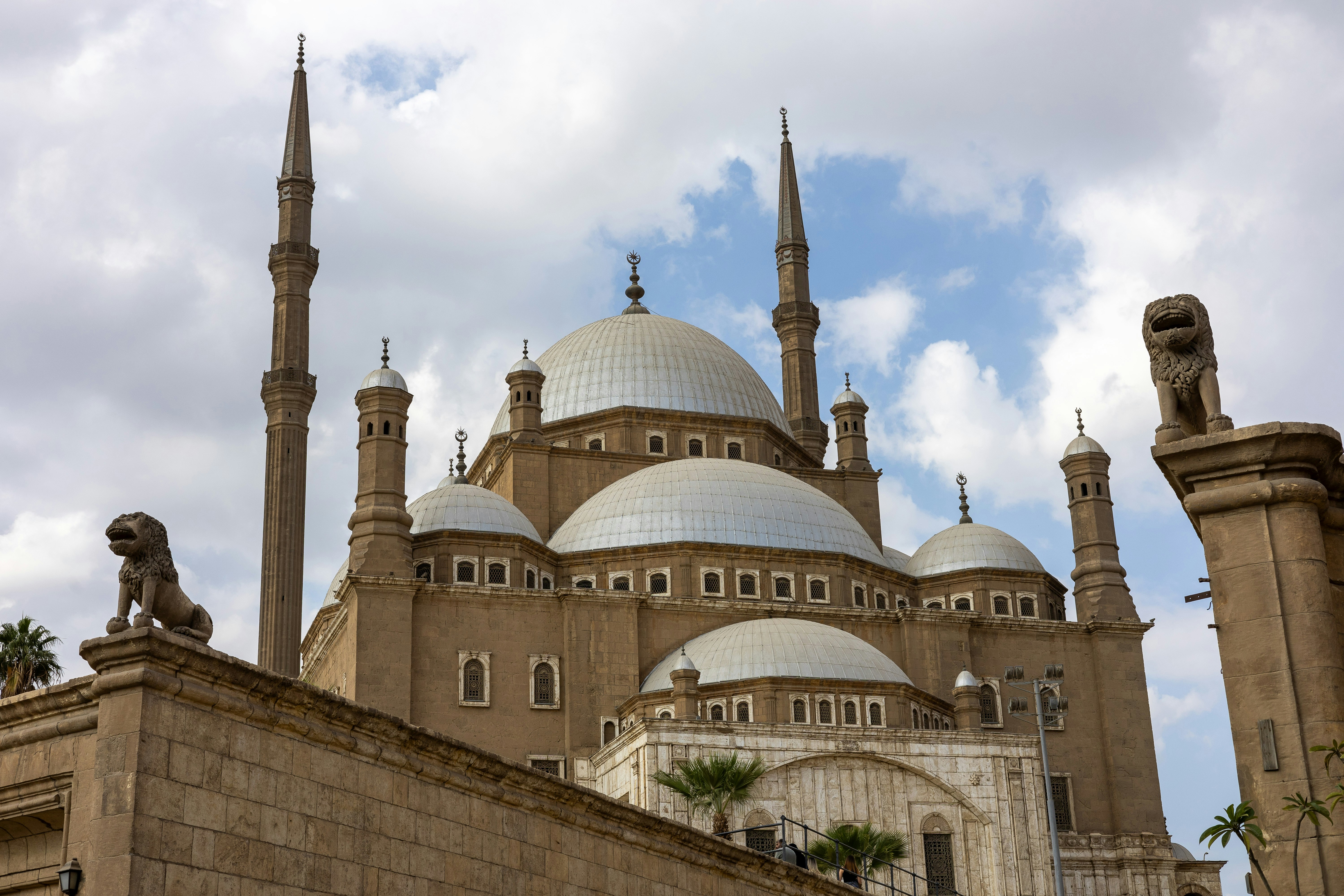 The Mohamed Ali Mosque's grand domes and minarets rise against a backdrop of clouds and blue sky, with earthy tones creating a serene contrast.