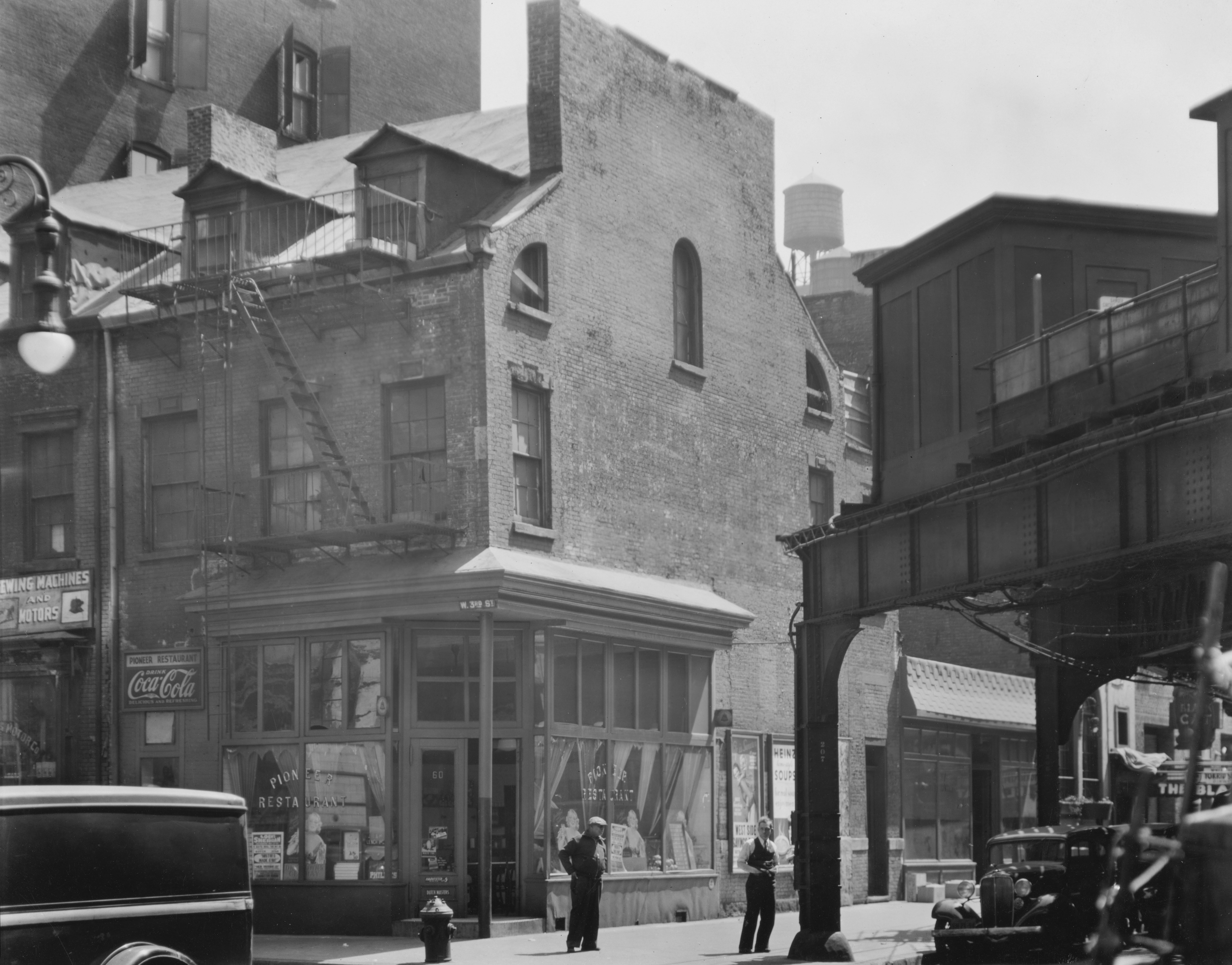 Monochrome urban street scene with a brick building, vintage ads, and a classic car, under interplay of light and shadow.