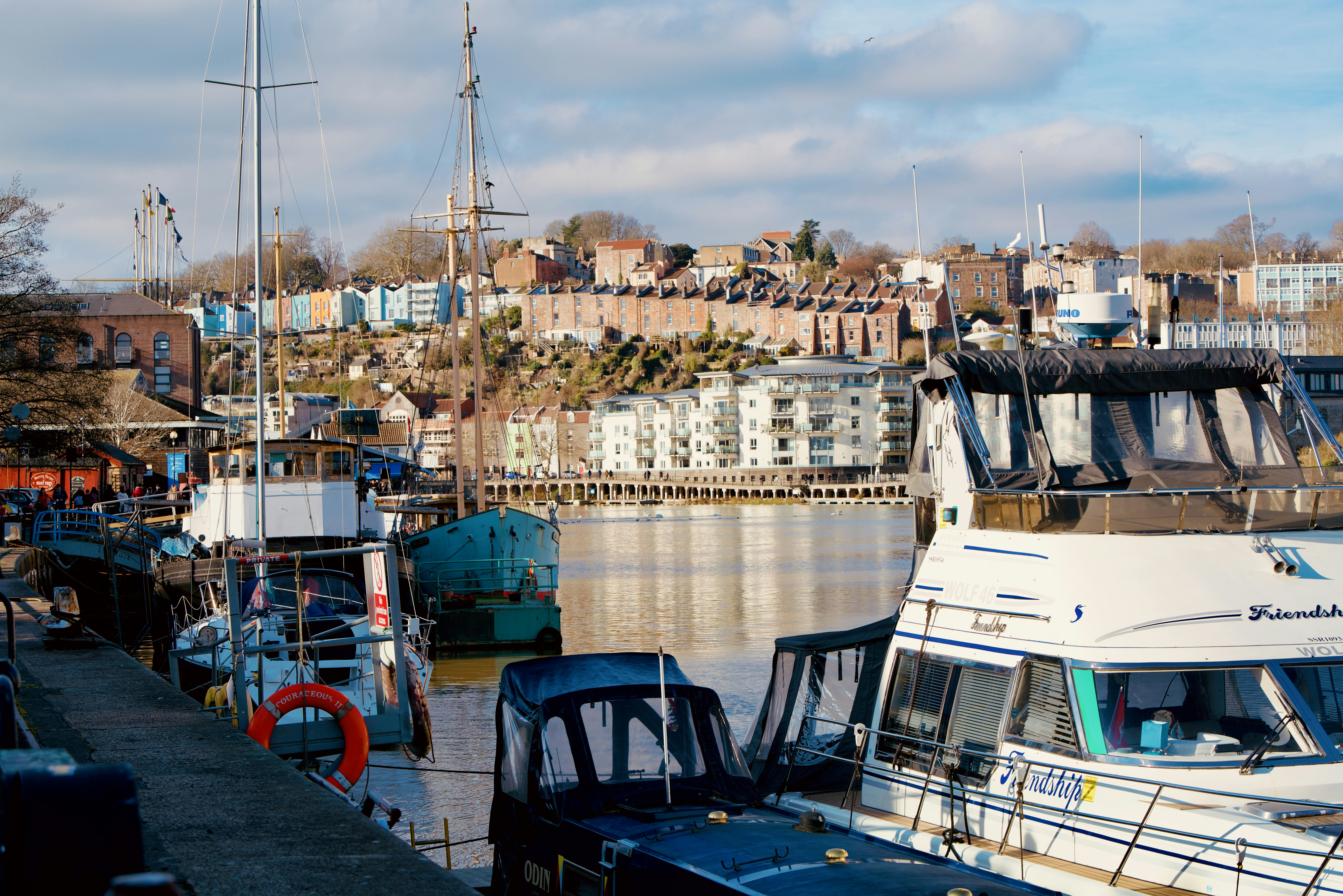 Boats docked in a lively harbor against colorful hillside buildings under a clear blue sky.