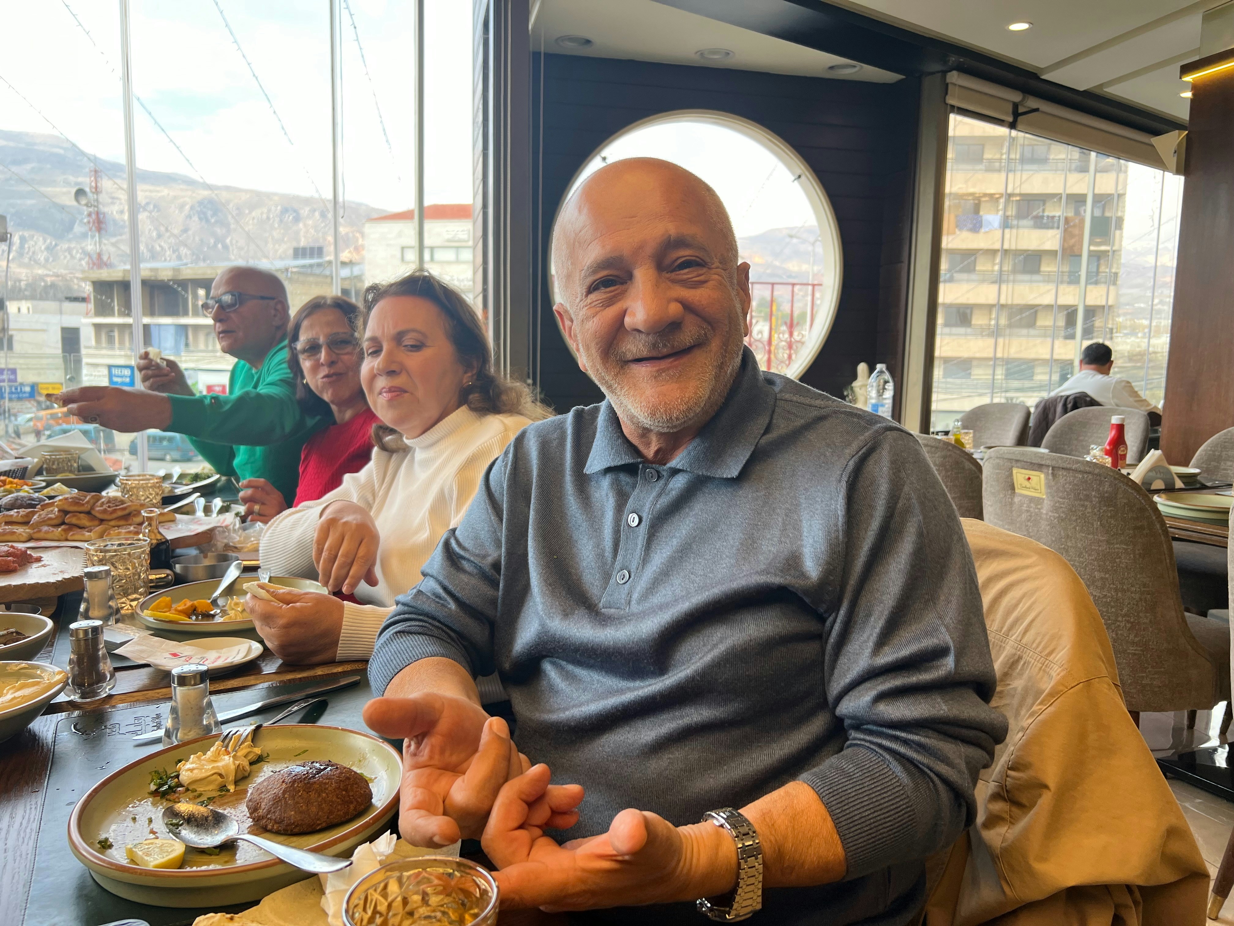 Group of friends dining in a restaurant with mountain views through large windows.