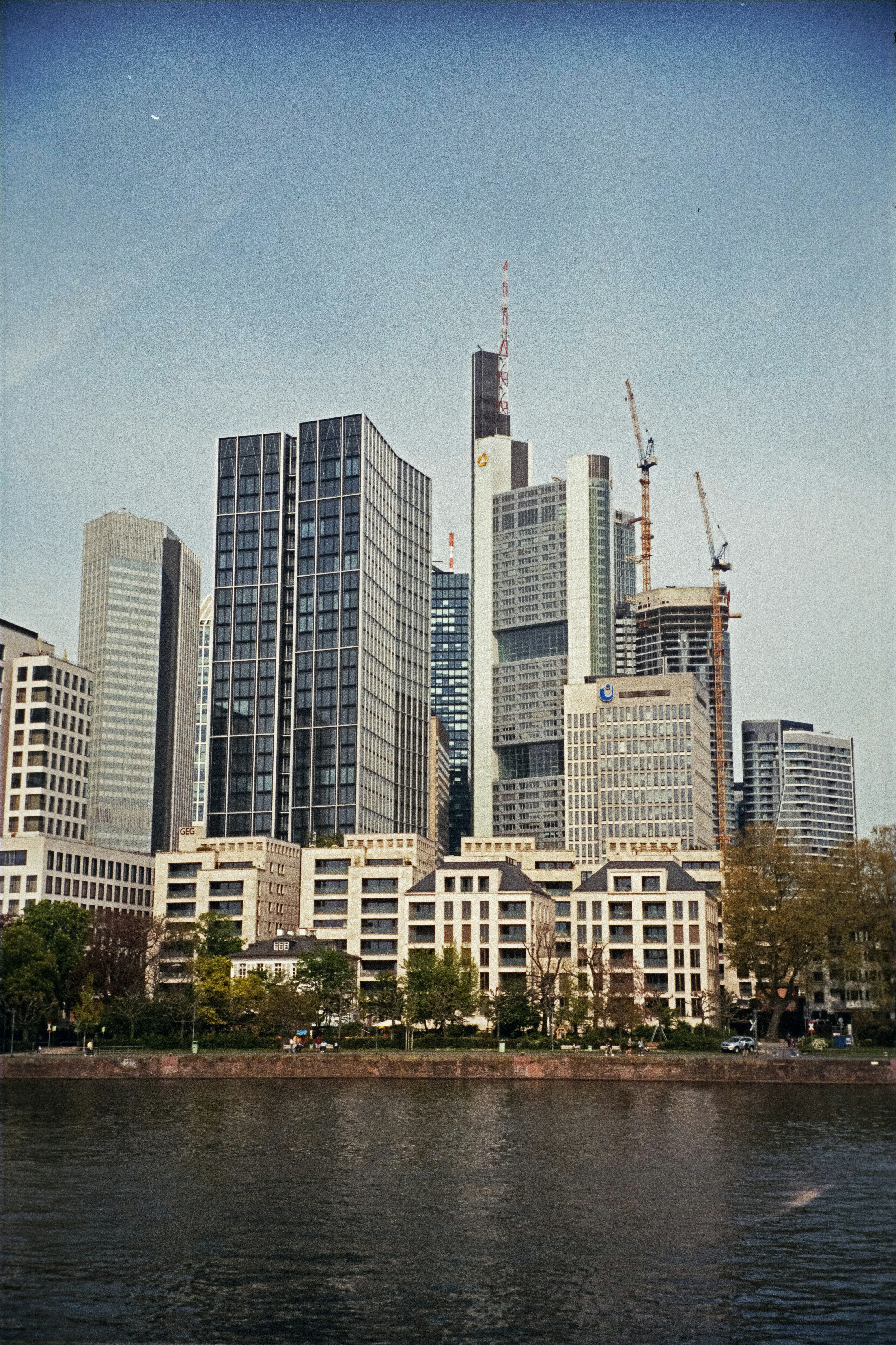 Modern skyscrapers rise along the riverbank under a clear sky.