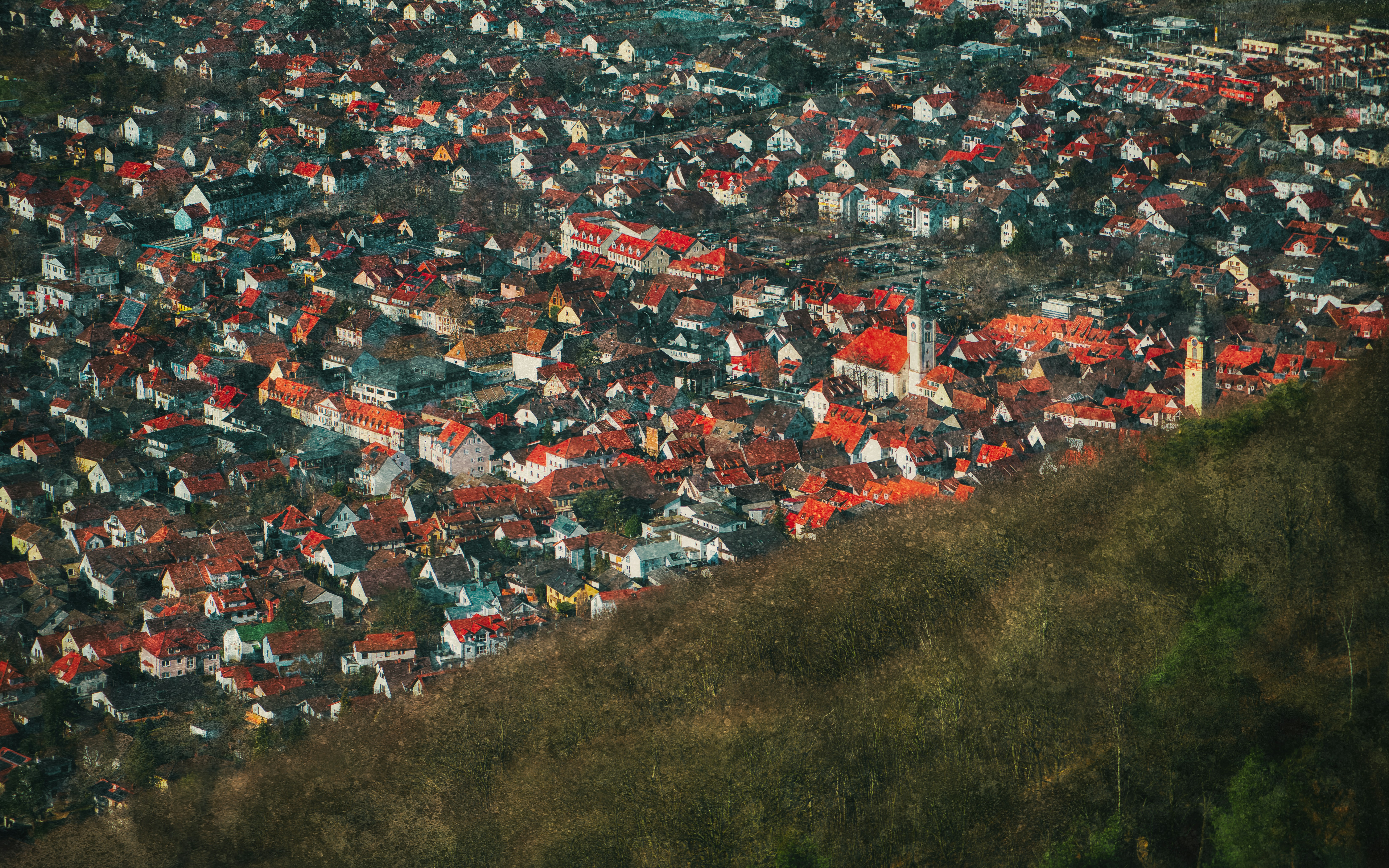 Aerial view of a village with colorful rooftops clustered densely against a hillside, contrasting with the surrounding greenery.