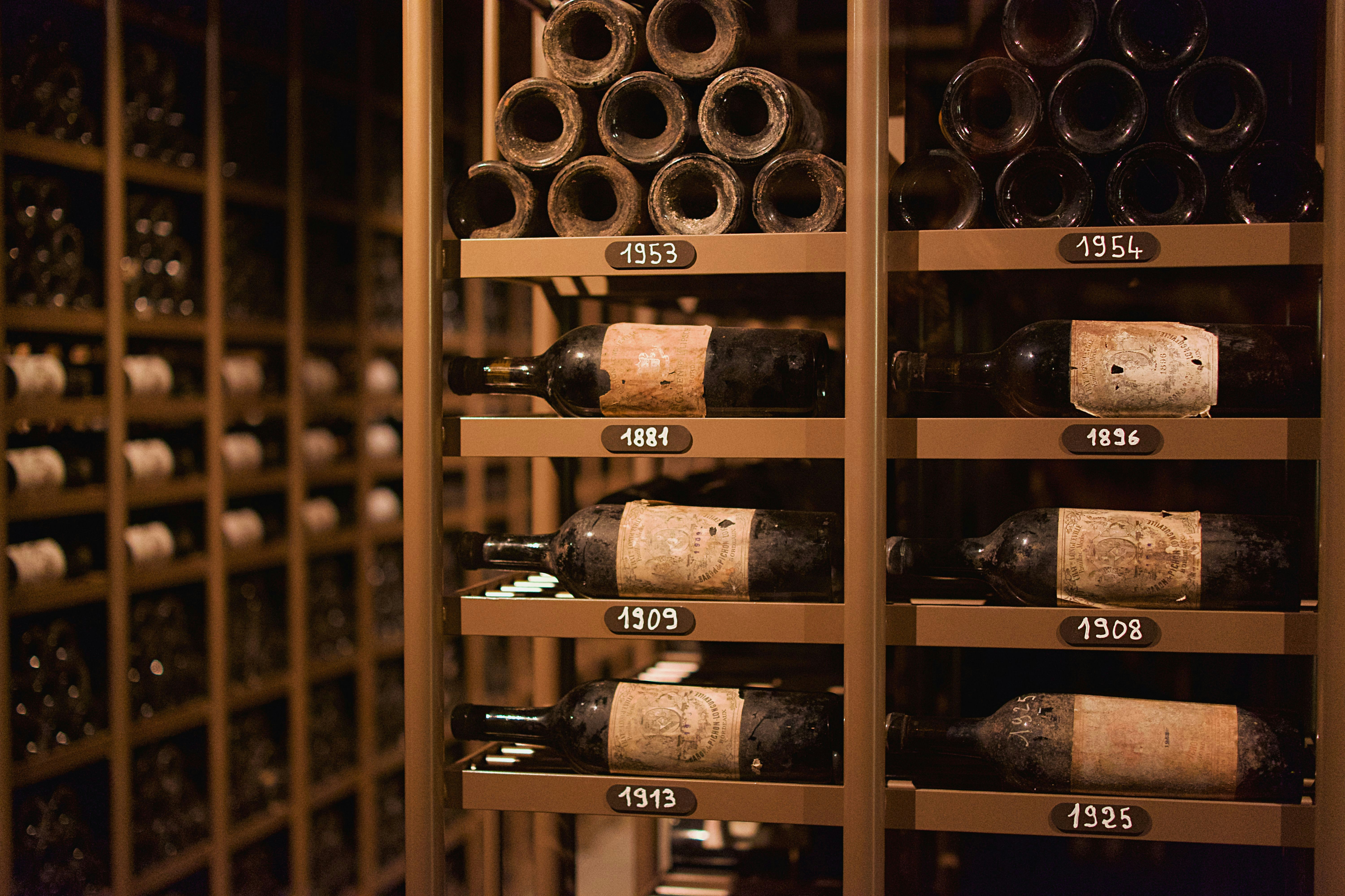 A collection of vintage wine bottles with aged labels, arranged neatly on wooden shelves in a dimly lit cellar.