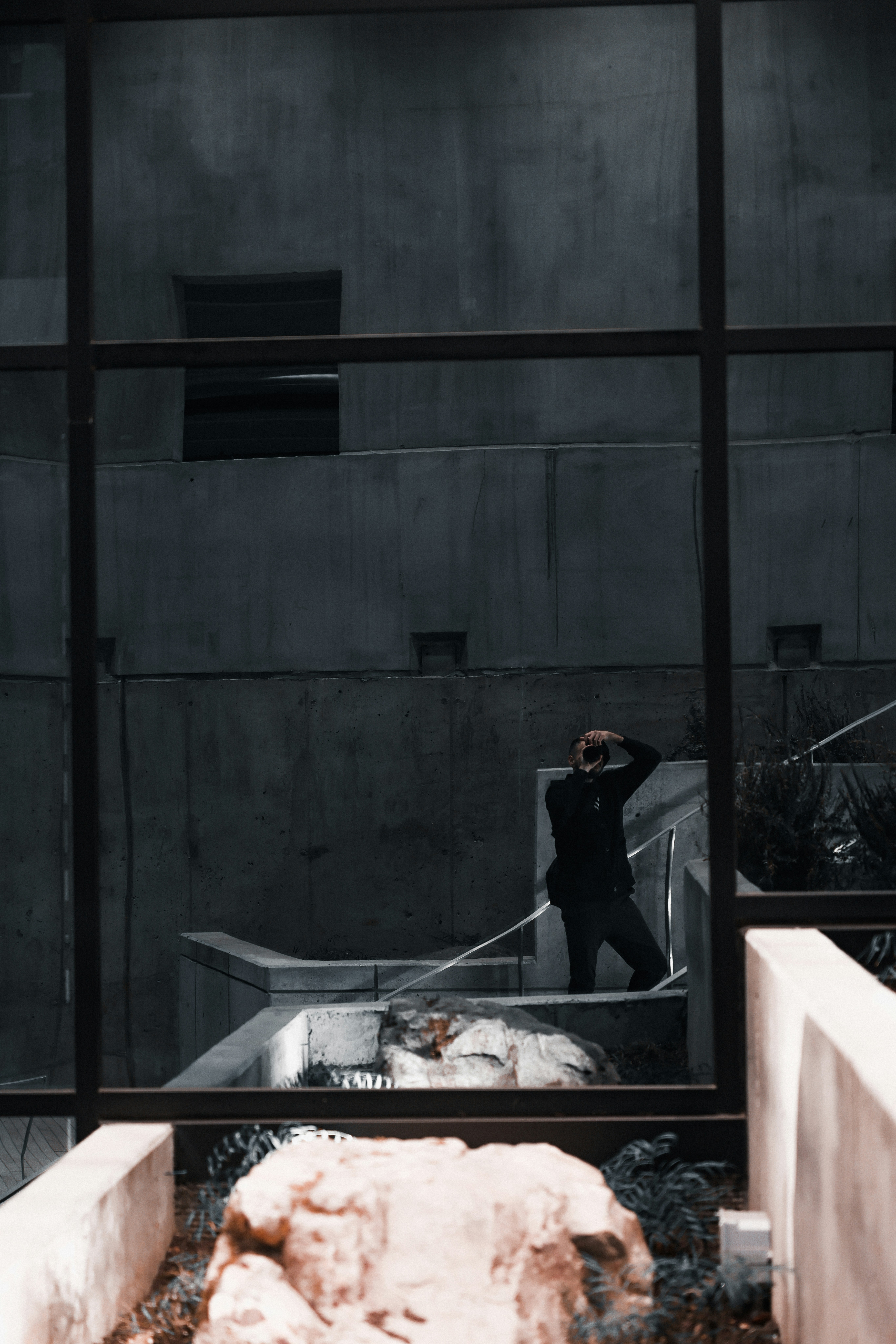 Person taking a photo through a reflective, grid-like window with concrete and stone elements.