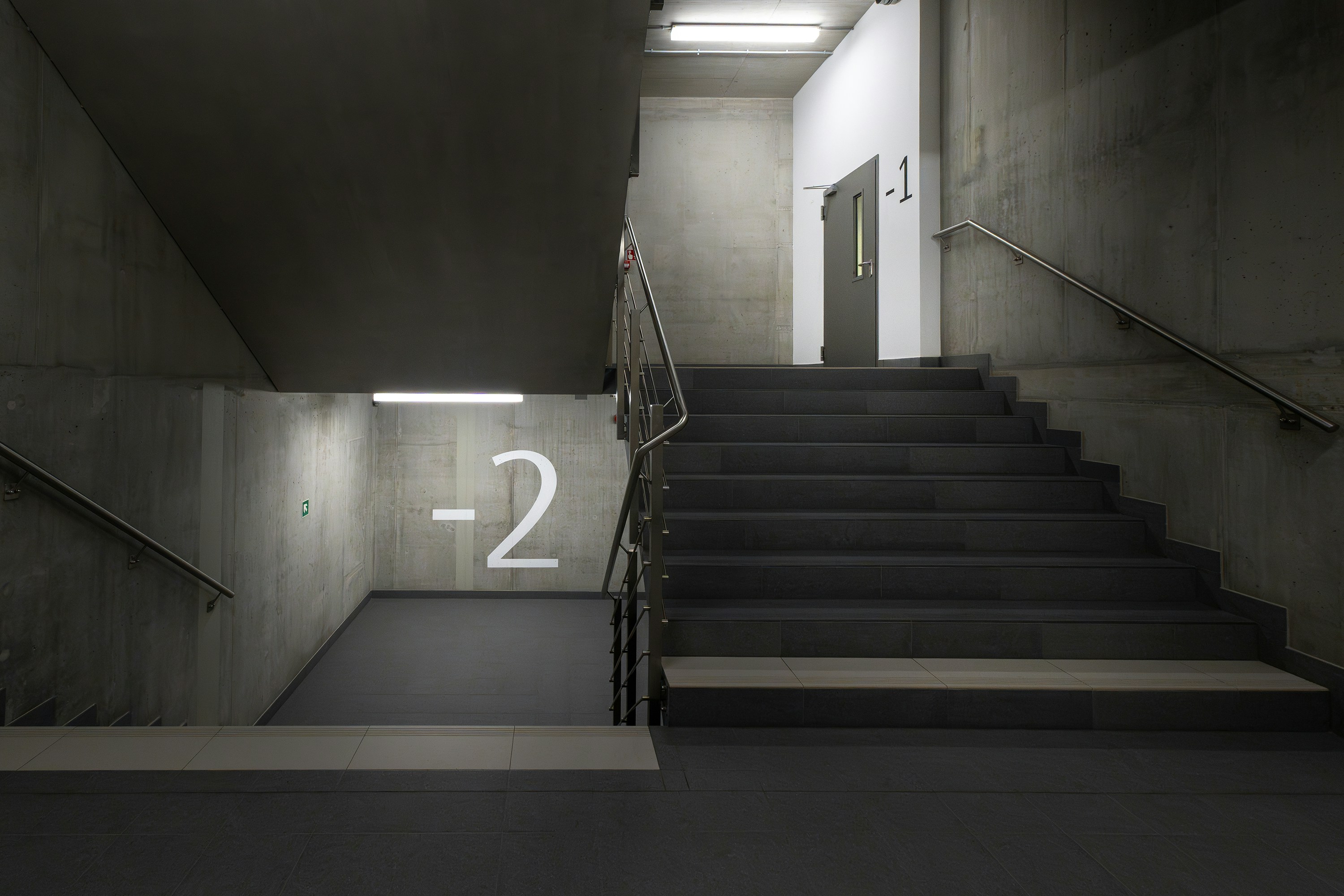 Industrial stairwell with minimalist lines and a subdued palette of grays and whites, featuring soft lighting and subtle shadows enhancing the architecture.
