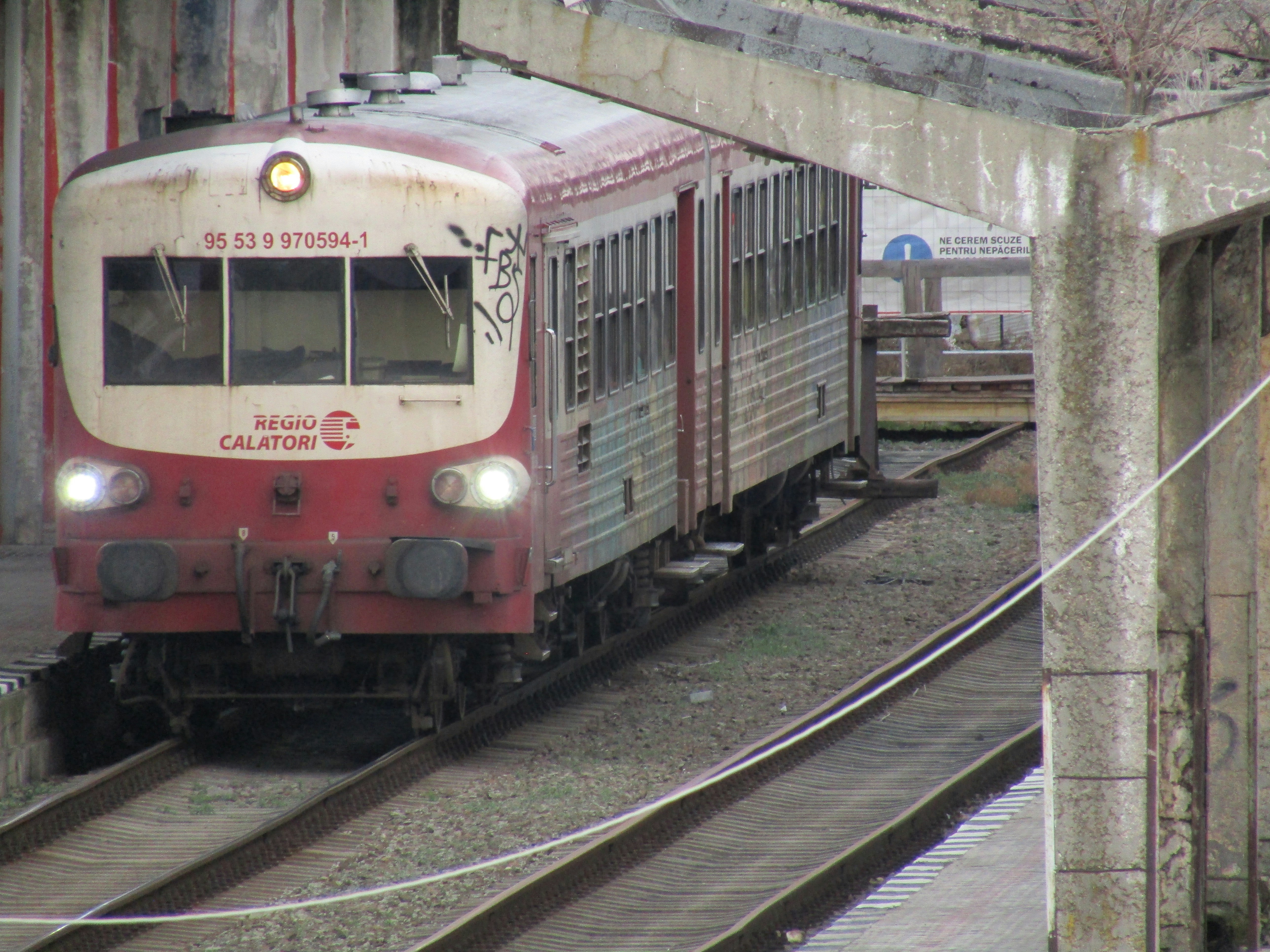 A graffiti-marked Italian railcar on a curved track beneath a concrete overpass, headlights aglow as it nears the camera.
