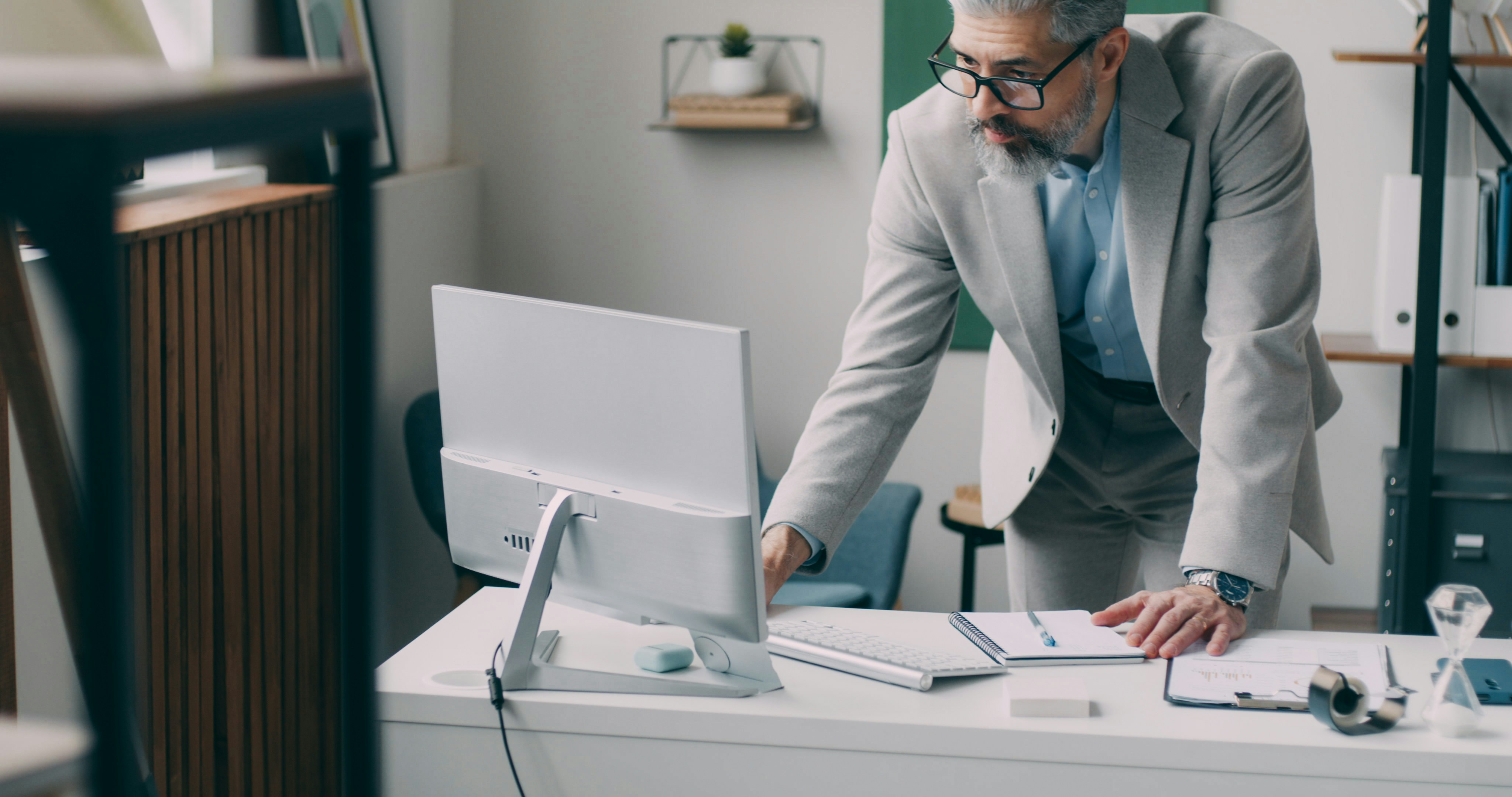 A man standing at a desk looking at a computer monitor photo – Free ...