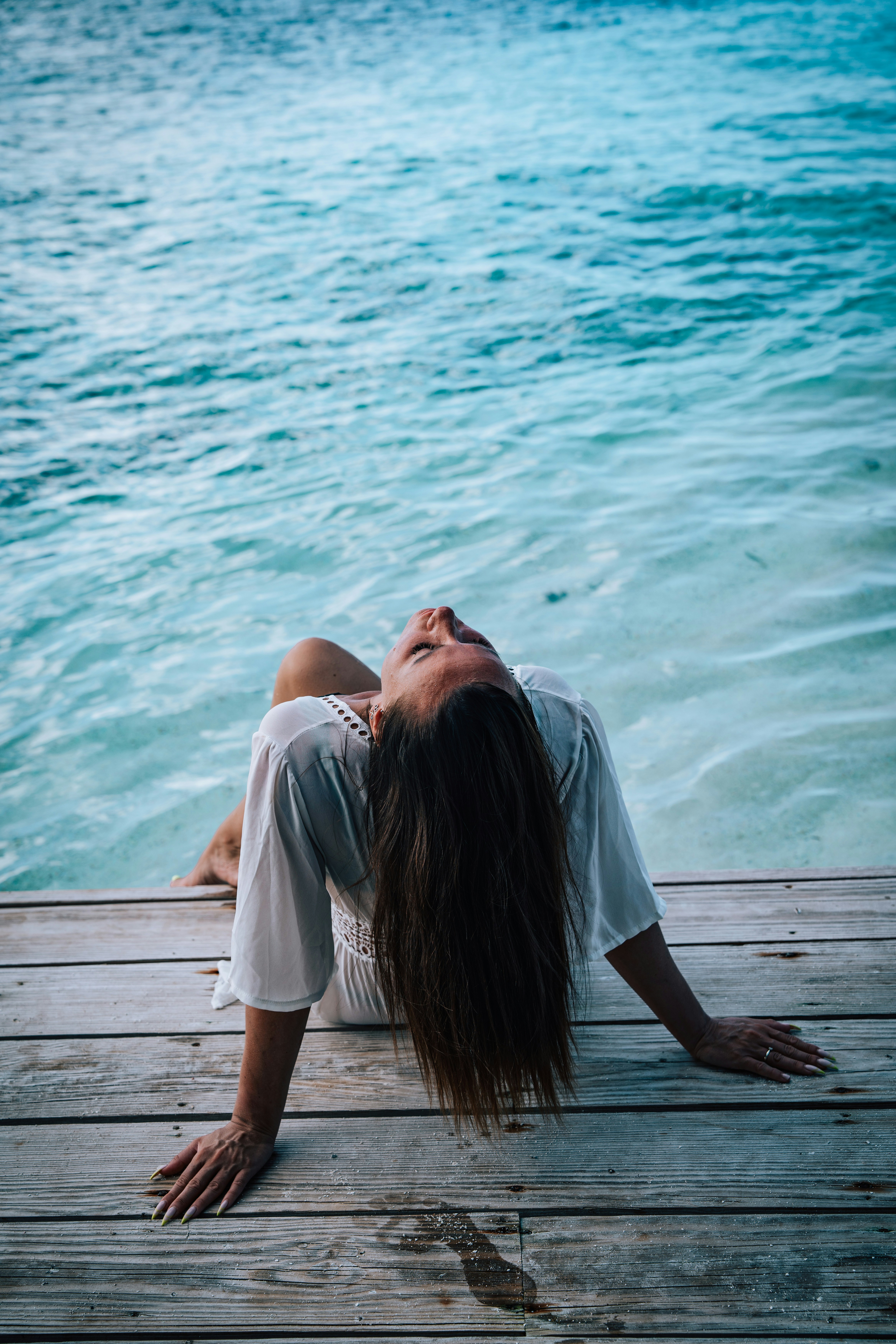 A woman laying on a dock next to a body of water photo – Free Woman ...