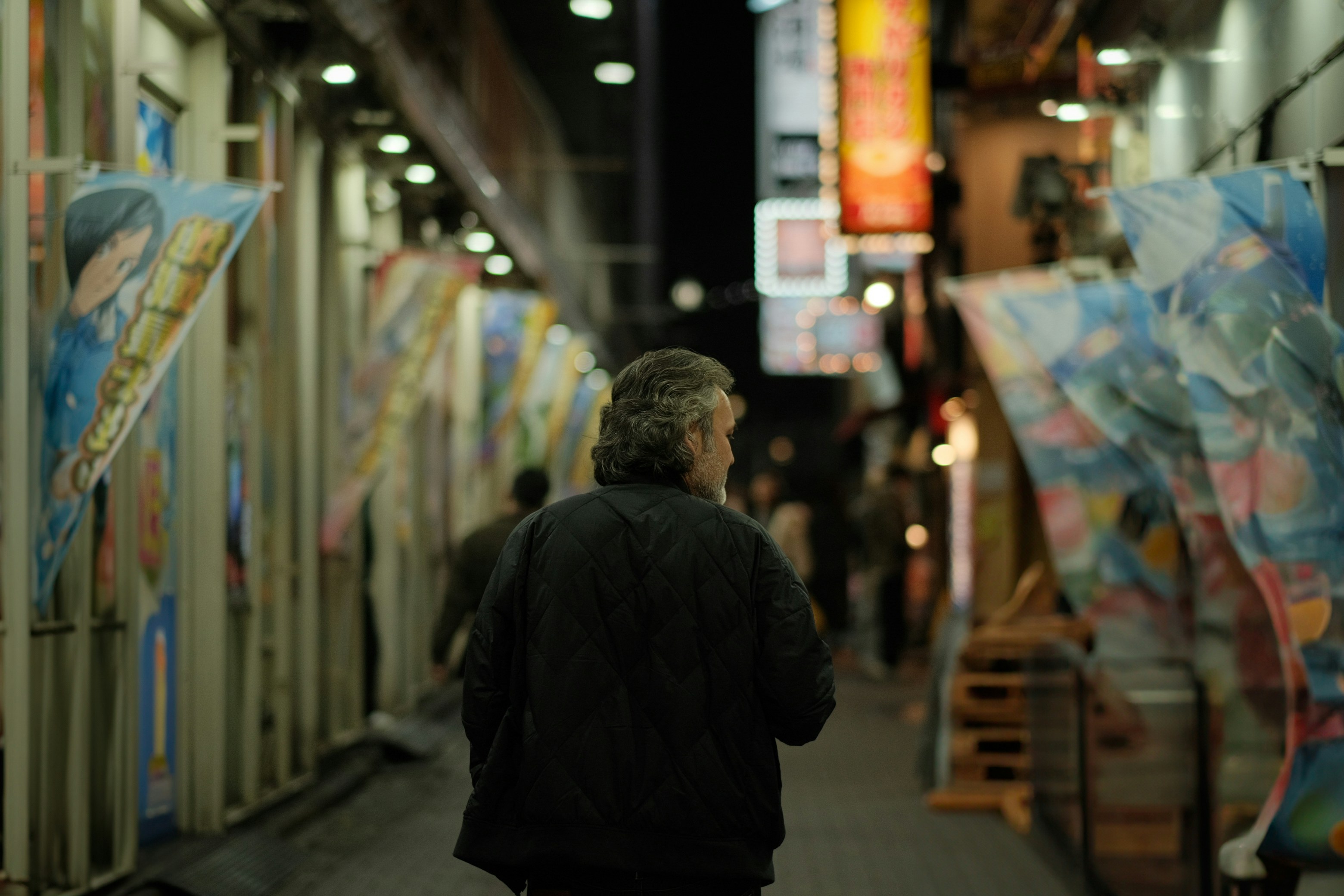 A person walks through a lively alley adorned with colorful banners and neon lights, amidst a softly lit atmosphere.