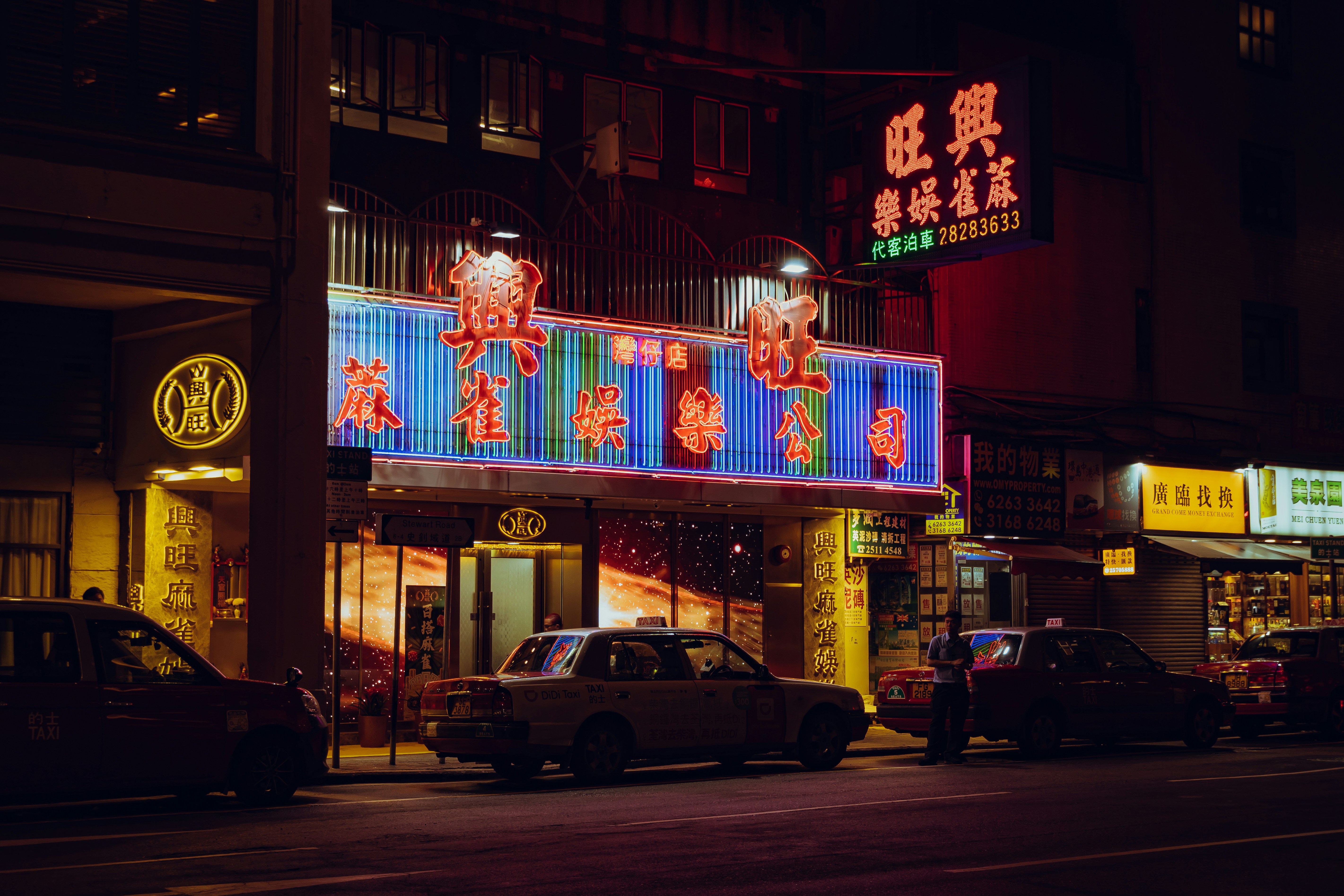 Vibrant neon signs illuminate a bustling urban street at night, with parked cars lining the road.