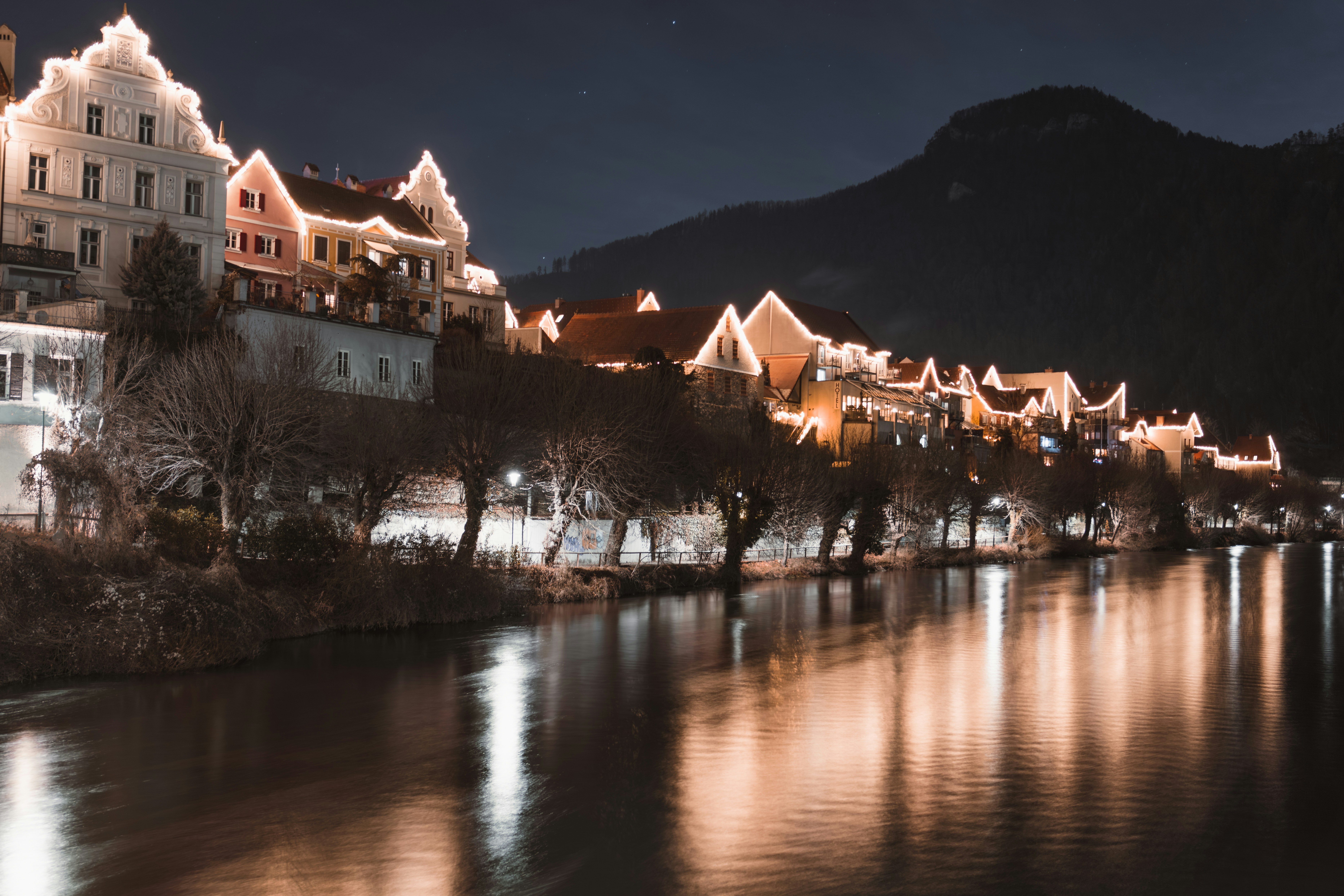 Riverbank Glow: Row of Gabled Townhouses Illuminated Along a Moonlit River