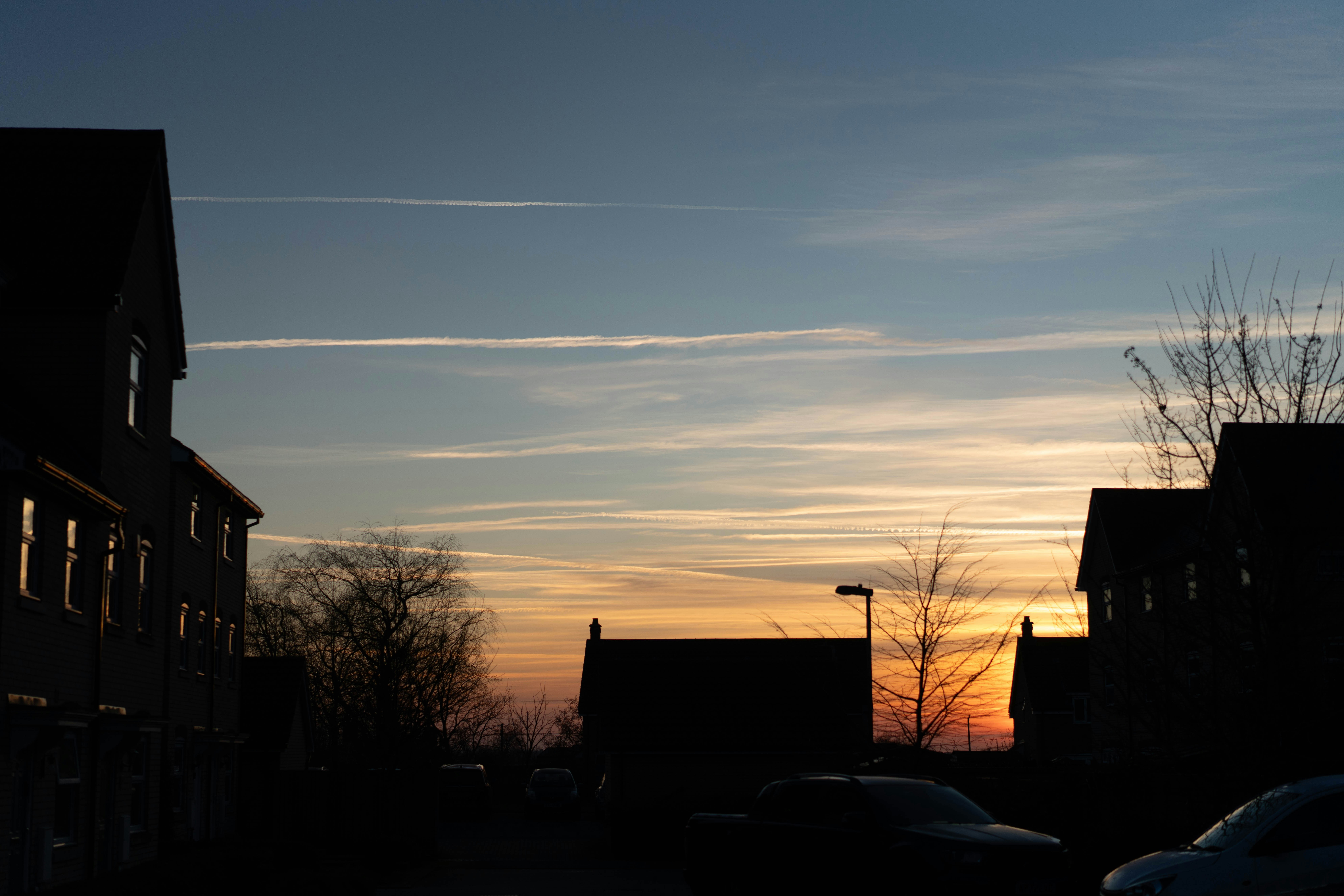 Silhouetted houses and trees against a gradient sunset sky of warm oranges and cool blues.