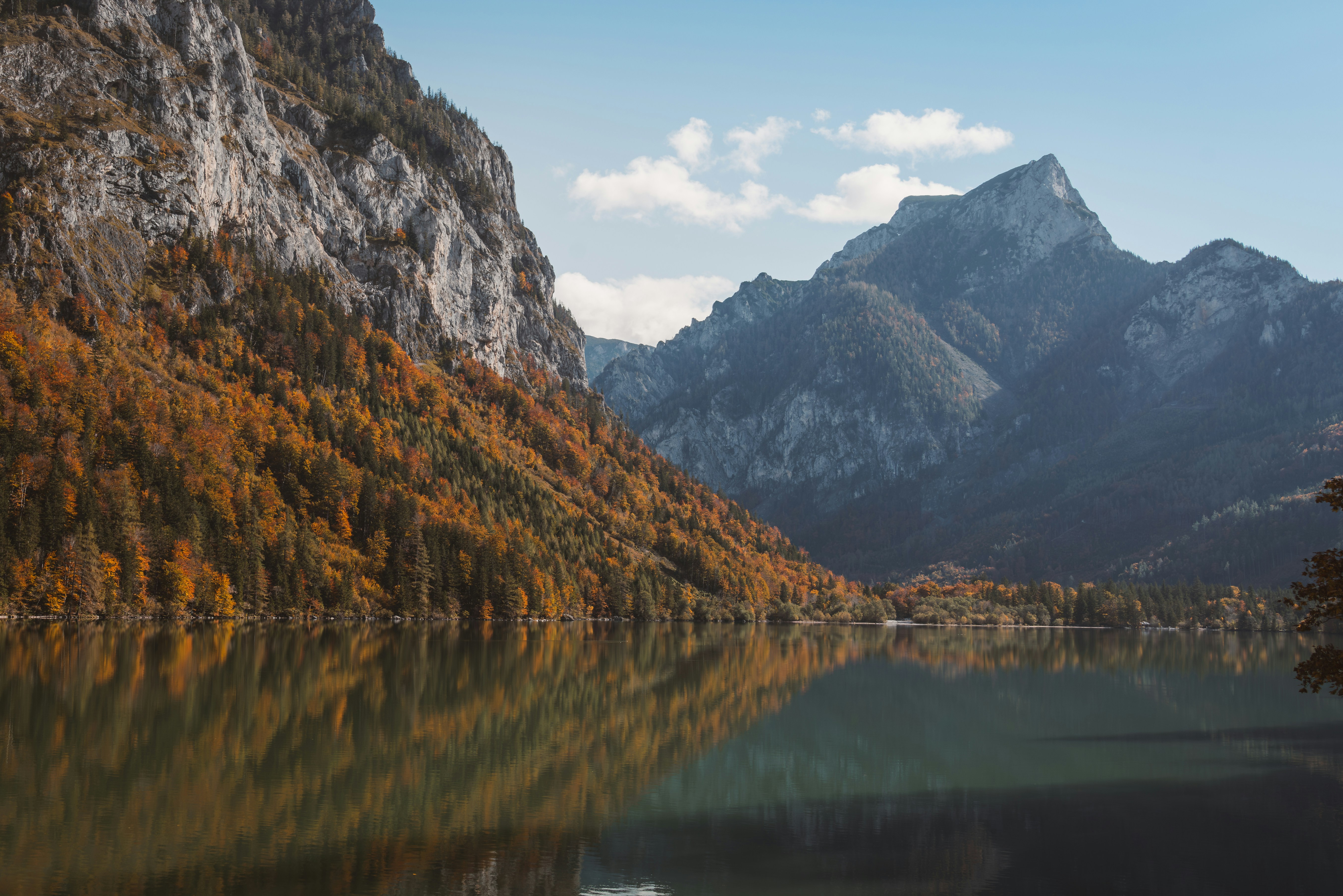 Mountain lake with vibrant autumn foliage and rocky peaks reflected on calm water under a clear sky.