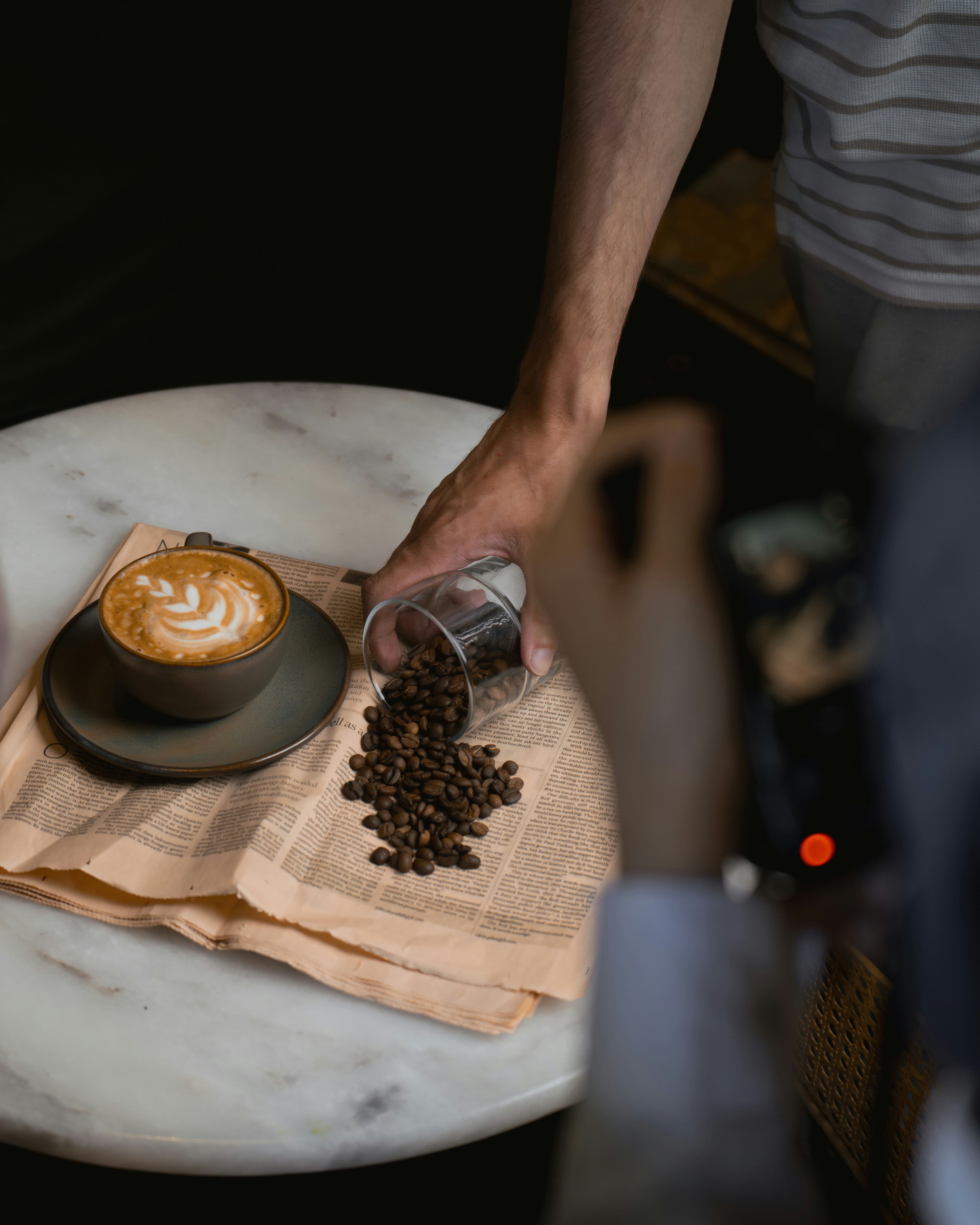 Barista’s Craft: Coffee Beans Pouring Onto Newspaper at a Marble Table