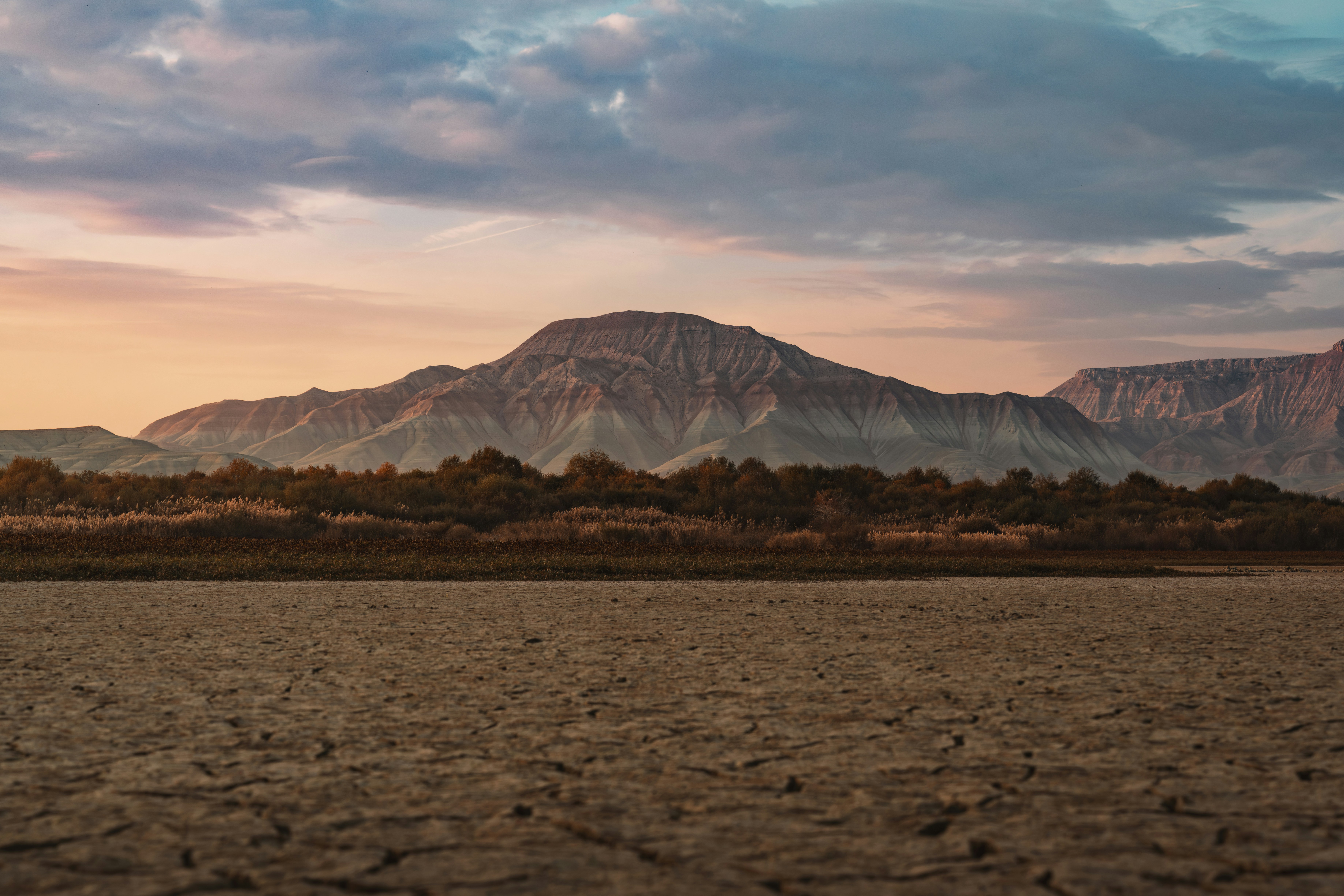 Mountain range at sunset with pink and orange sky above cracked barren land.