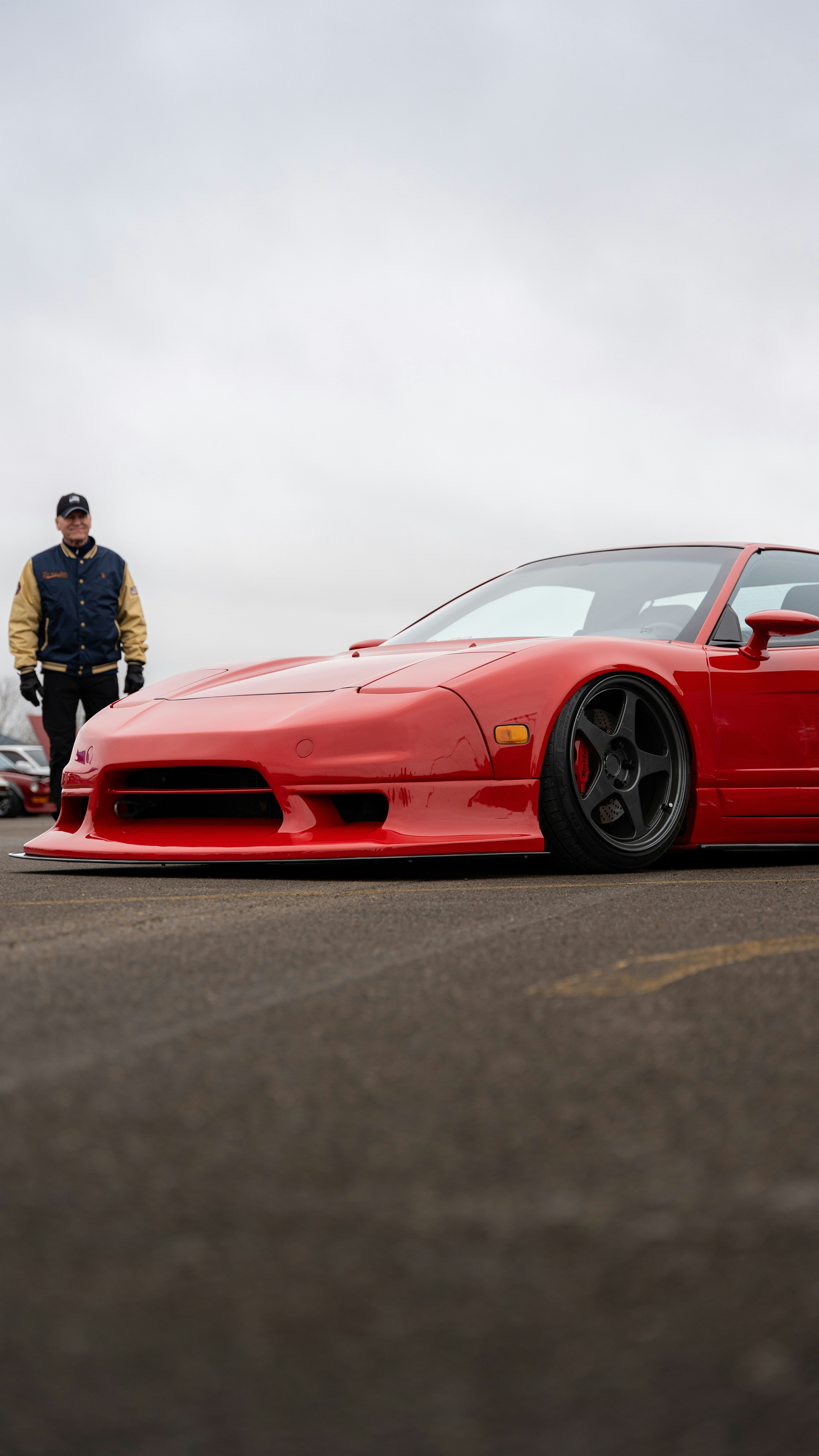 Red NSX parked with a spectator nearby under a grey sky.