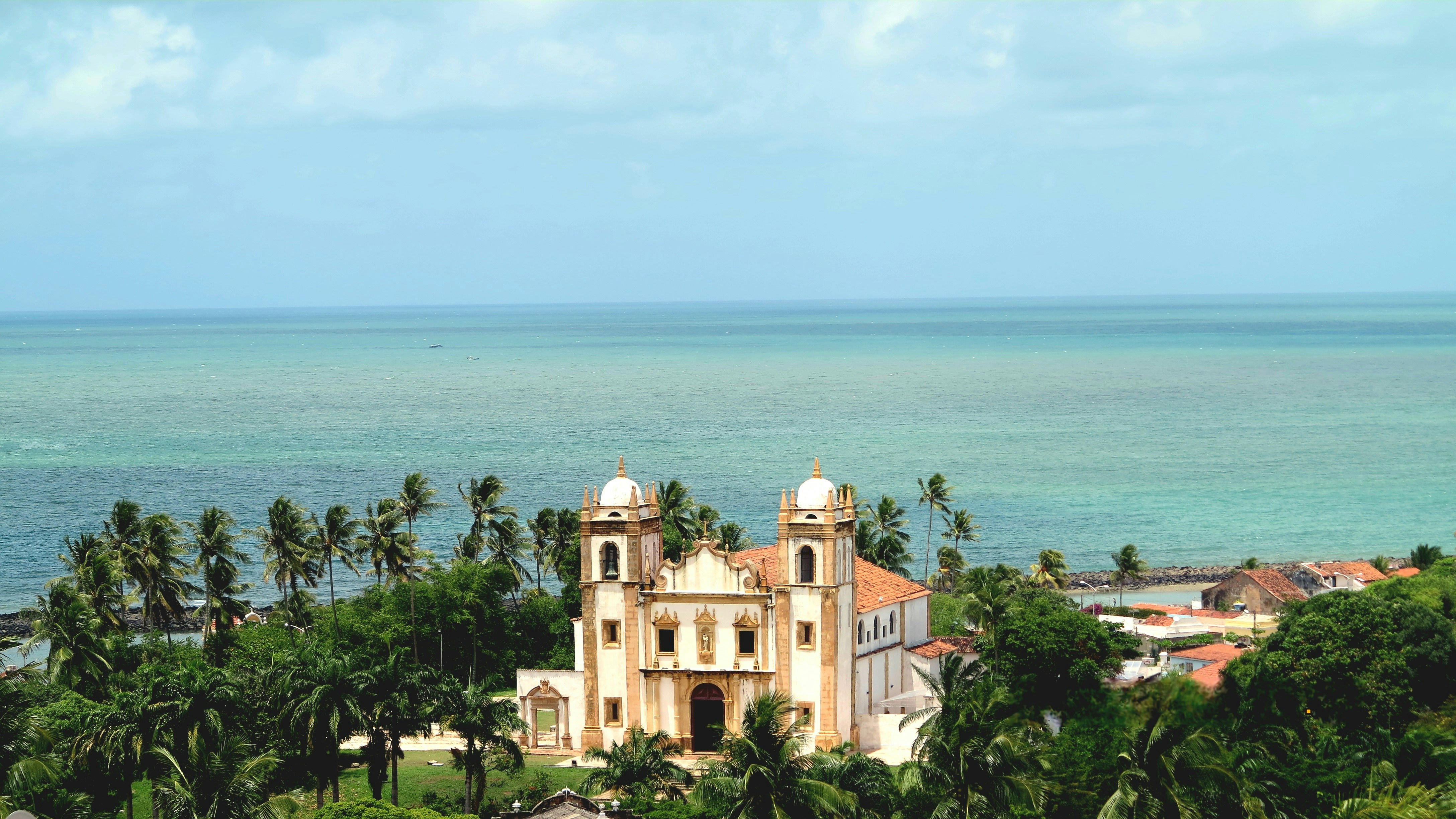 Carmo de Olinda Church nestled among lush greenery with the turquoise sea in the background.