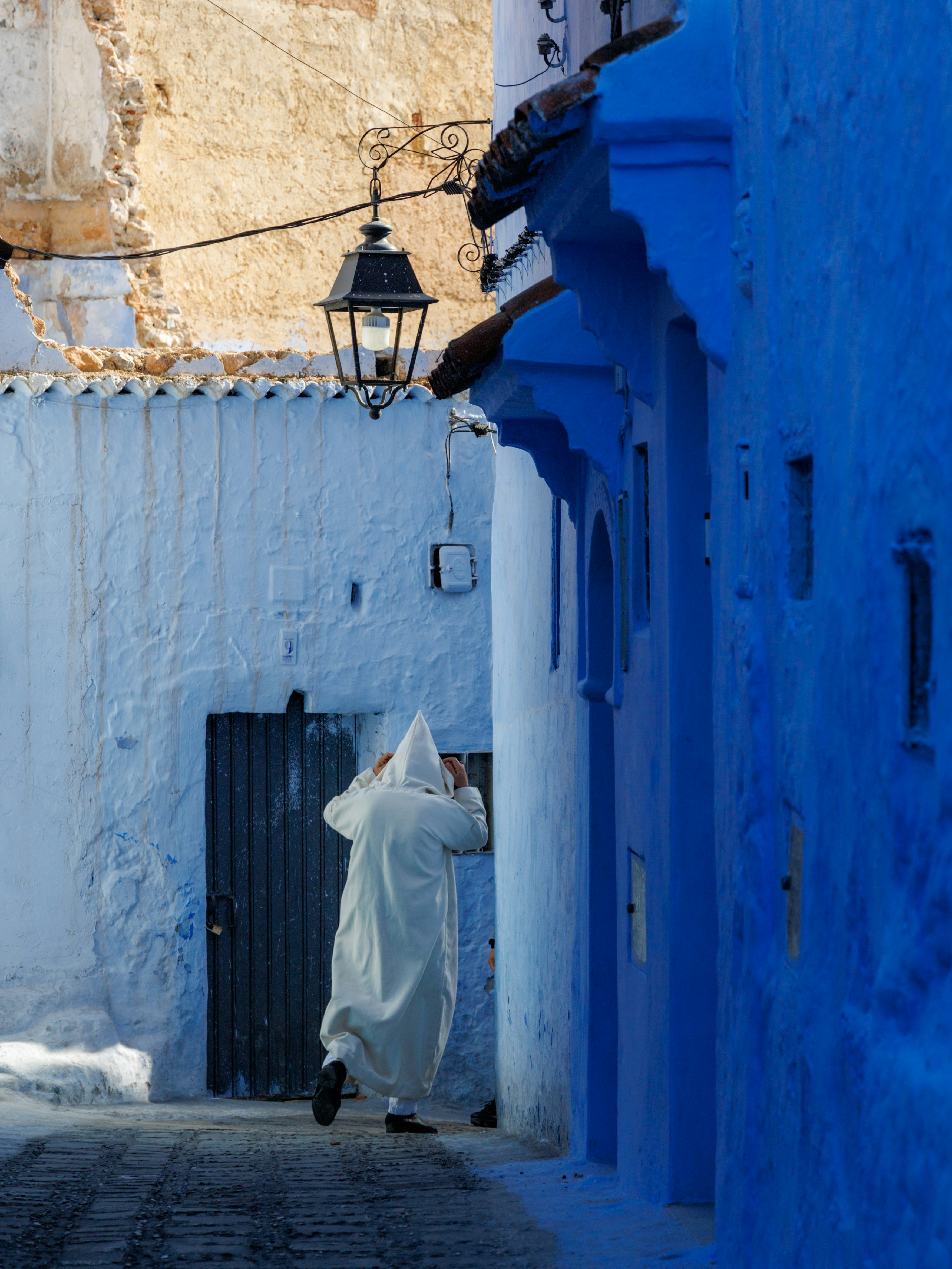 A man in white djellaba walking through the street of Chefchaouen, Morocco.